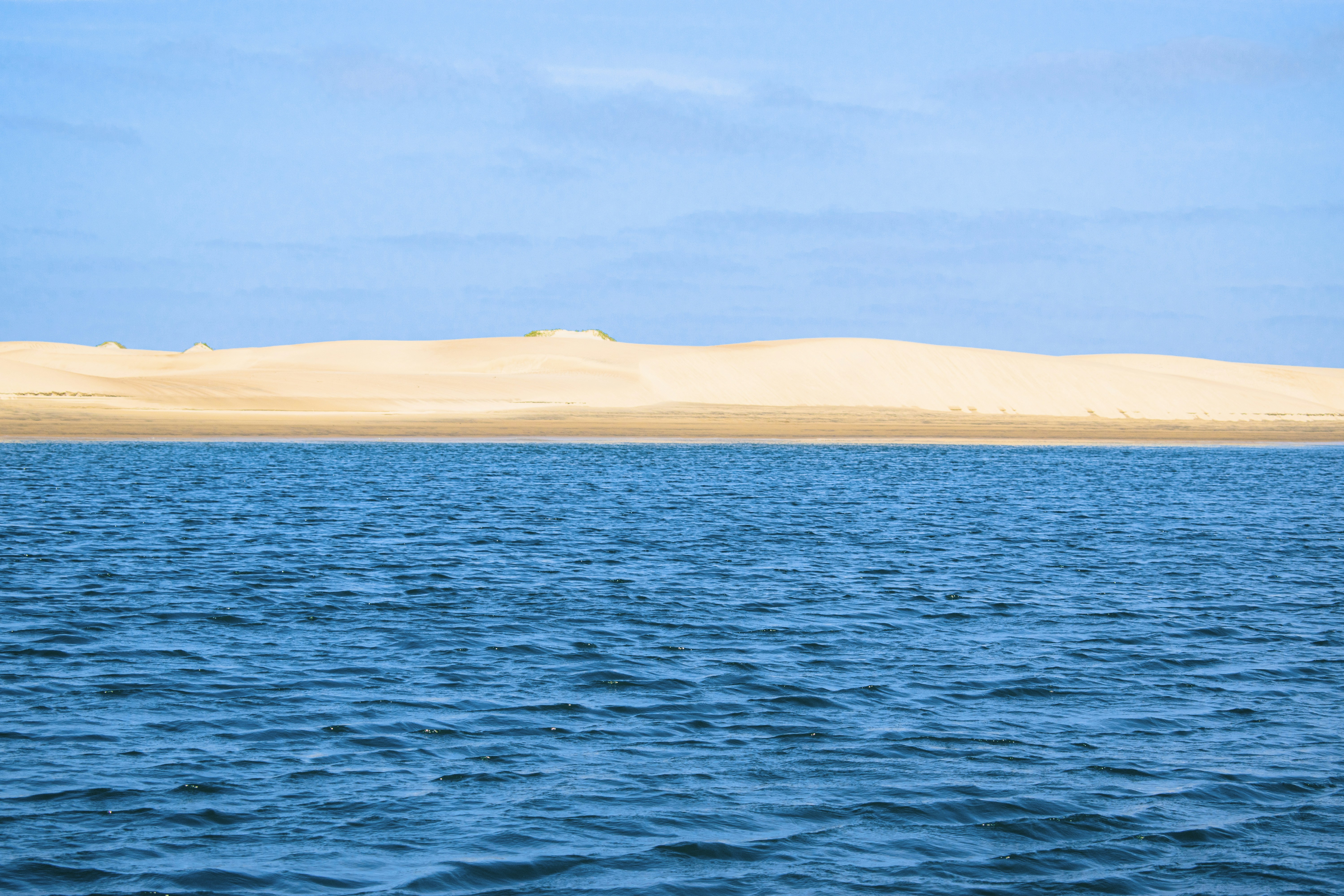 Vast expanse of tranquil blue water contrasting with golden sand dunes under a clear sky.