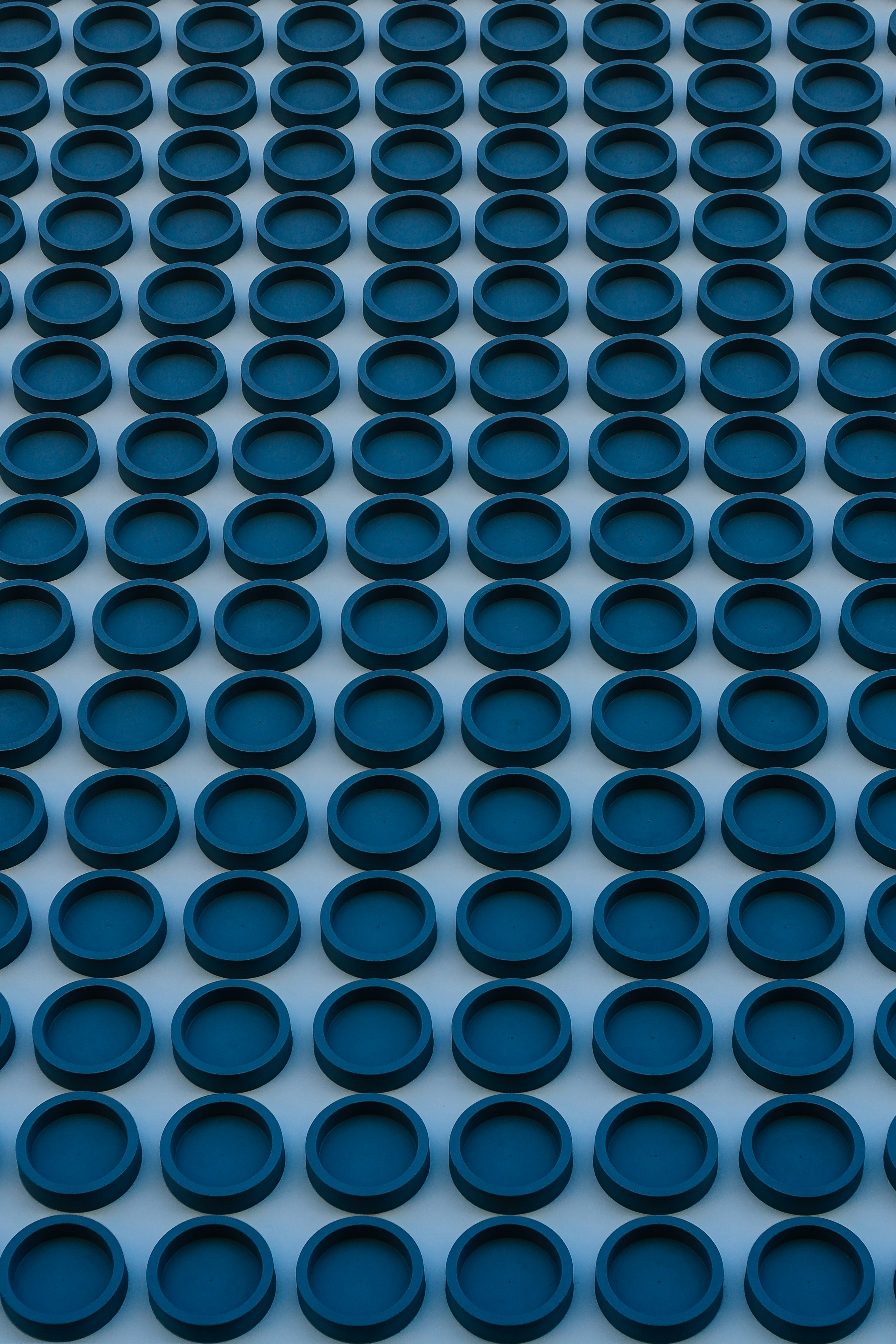 A grid of blue circular objects arranged meticulously on a flat surface, creating a rhythmic pattern. The uniformity highlights the interplay of shapes and colors.