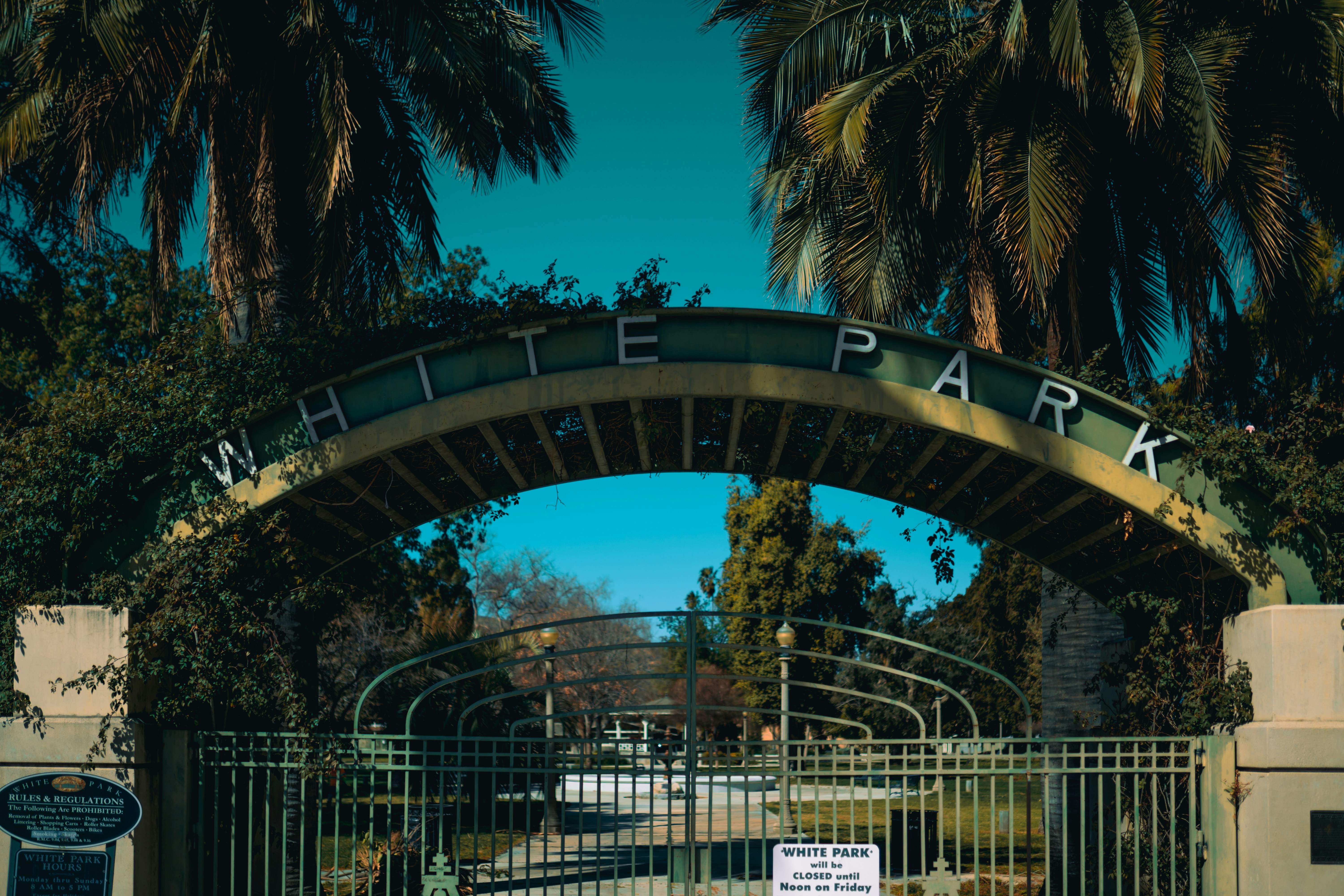 Archway of White Park adorned with lush greenery and palm trees, inviting visitors to explore the serene pathways beyond.