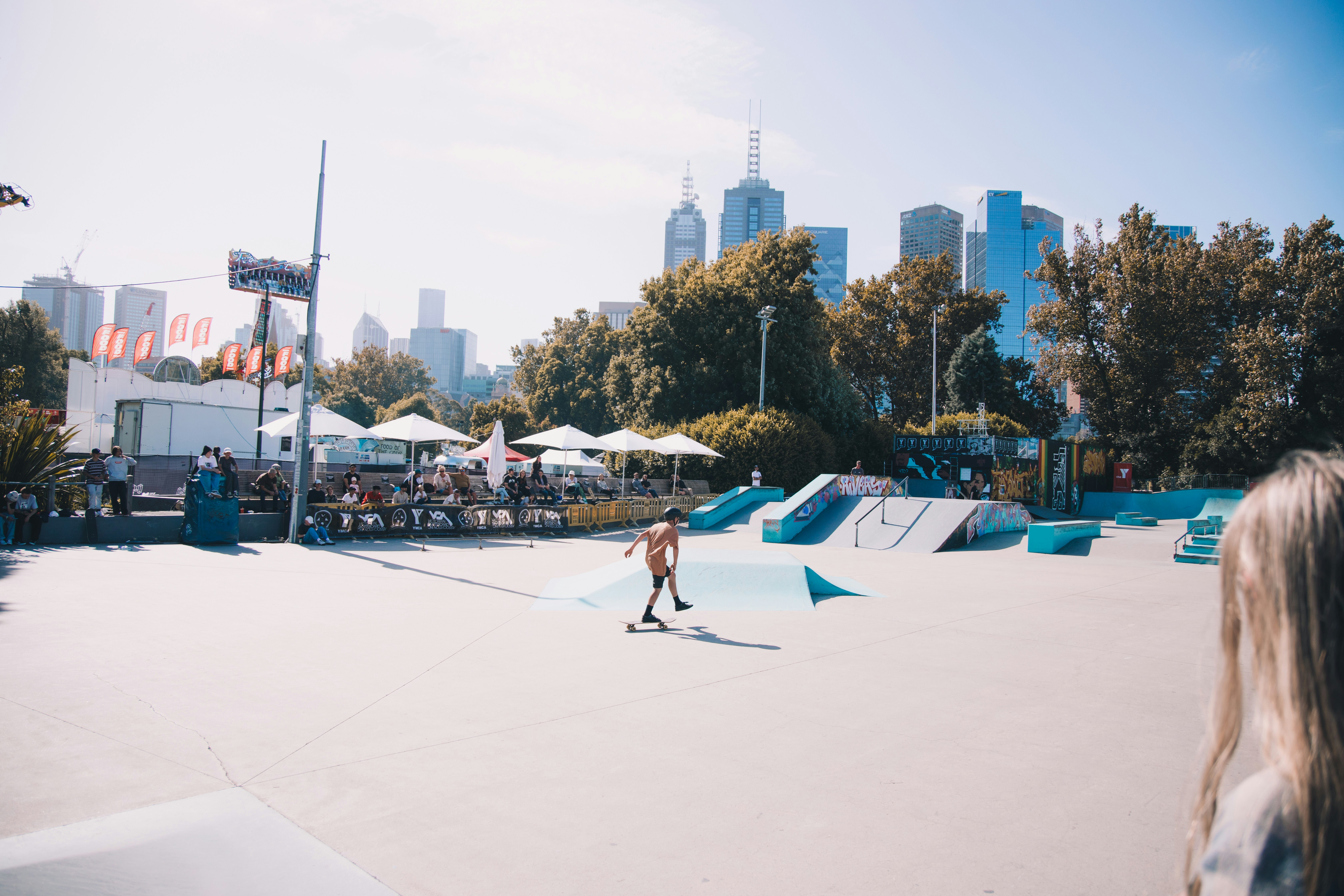 Skateboarder navigating ramps in a sunlit urban park with skyscrapers in the background.