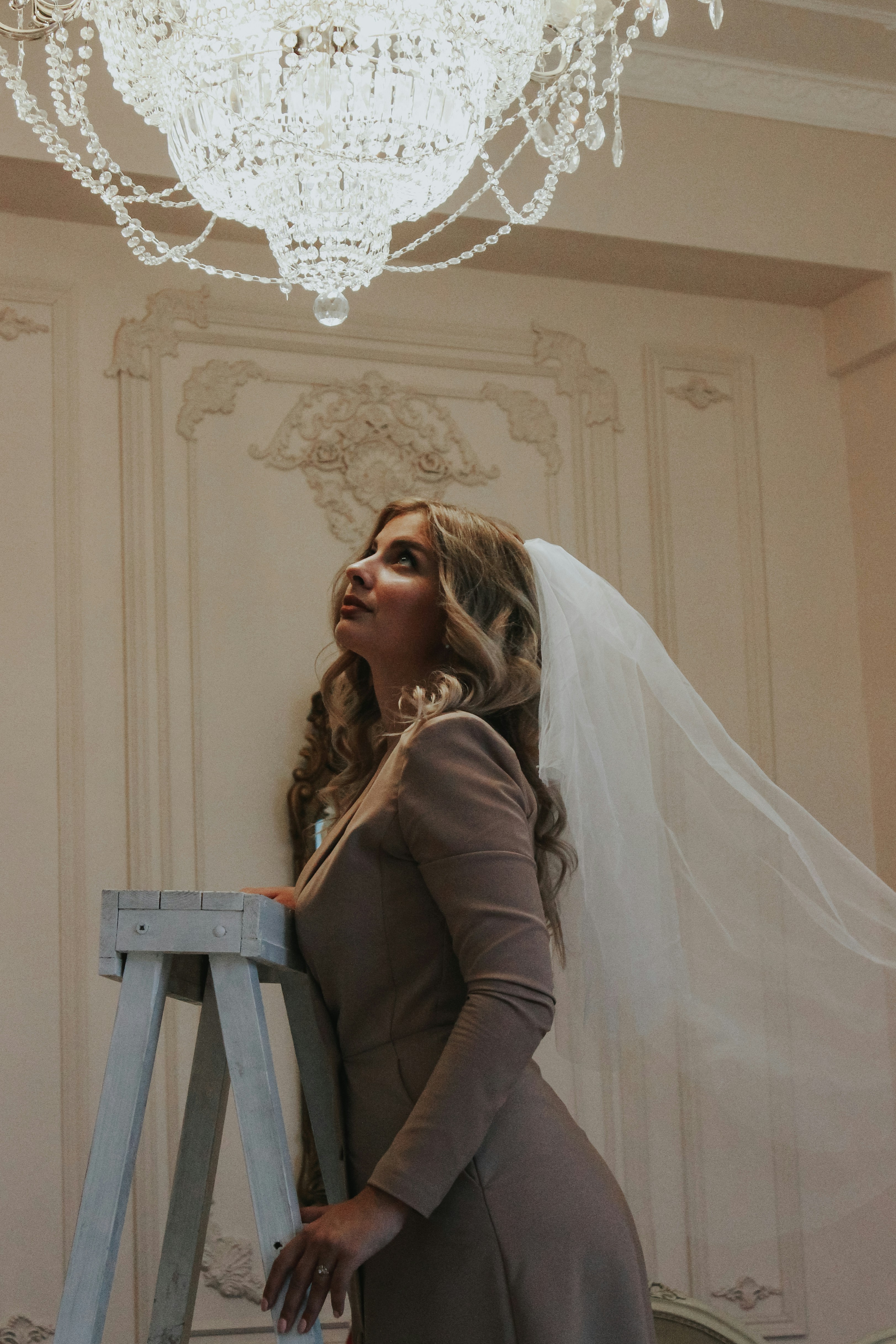 Gilded Glow: Bride Beneath a Crystal Chandelier in an Ornate Interior