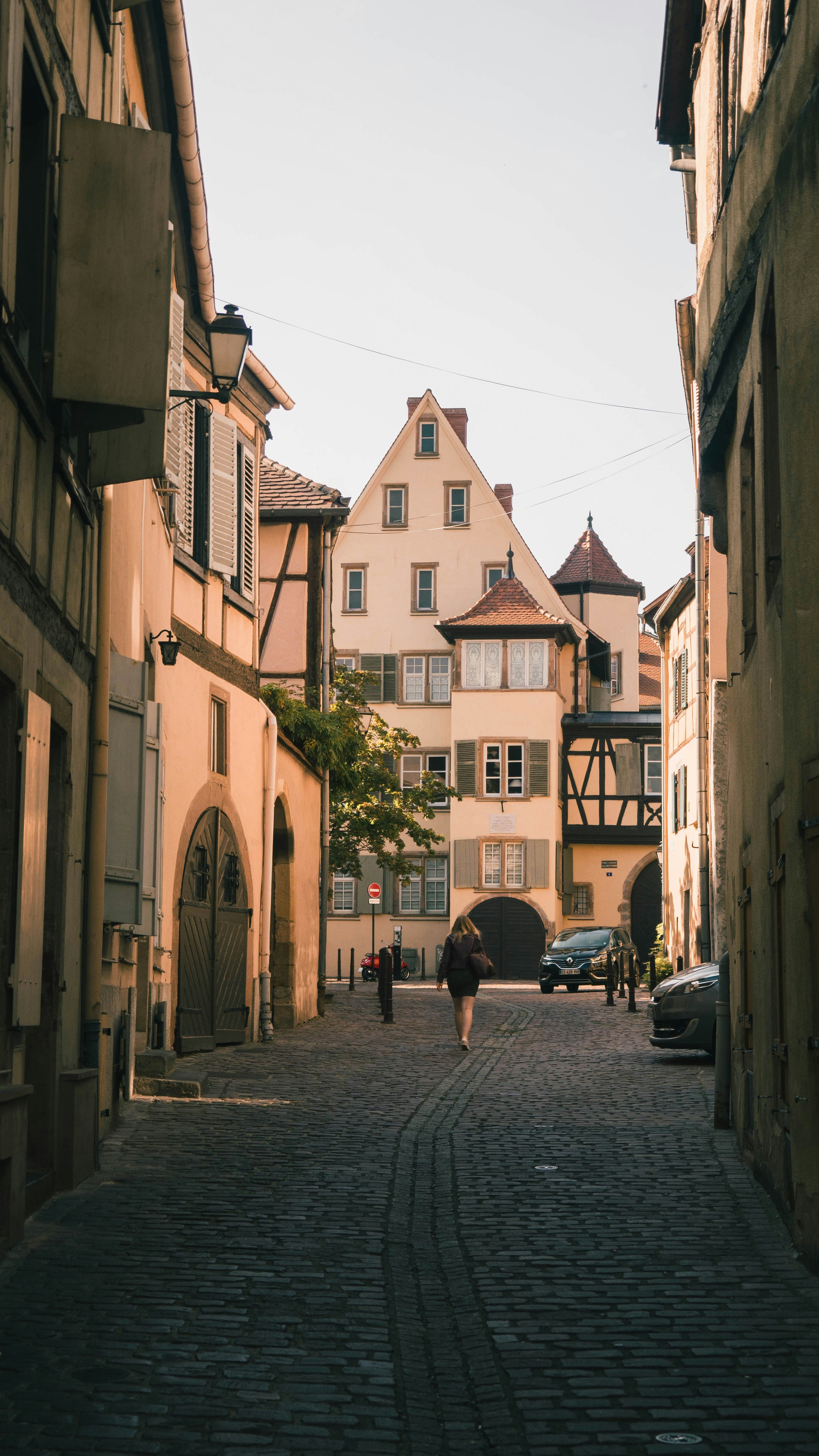 Charming narrow street lined with historic buildings, leading to a picturesque square with a unique architectural structure.
