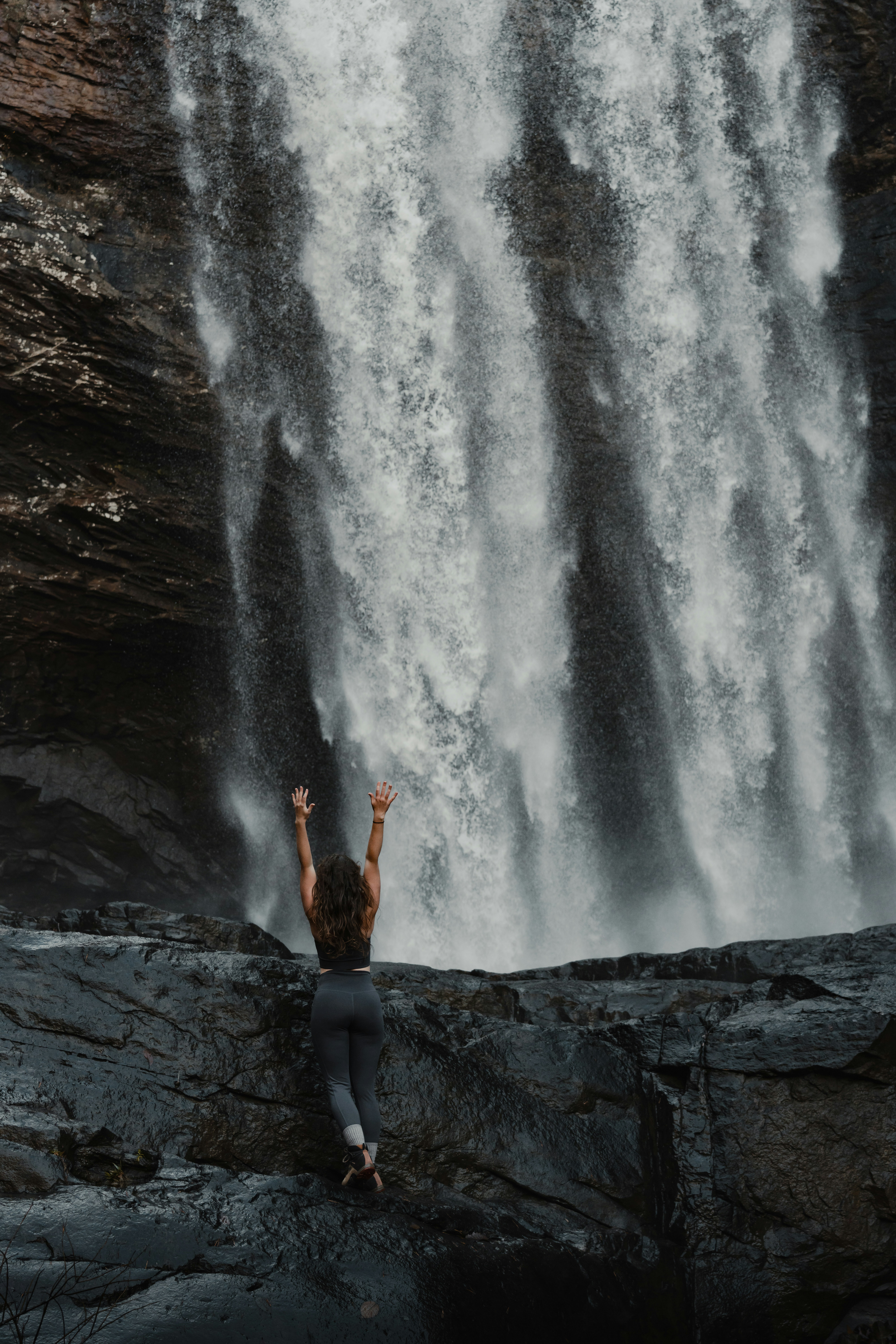 Person in black pants standing on rock in front of waterfalls during ...