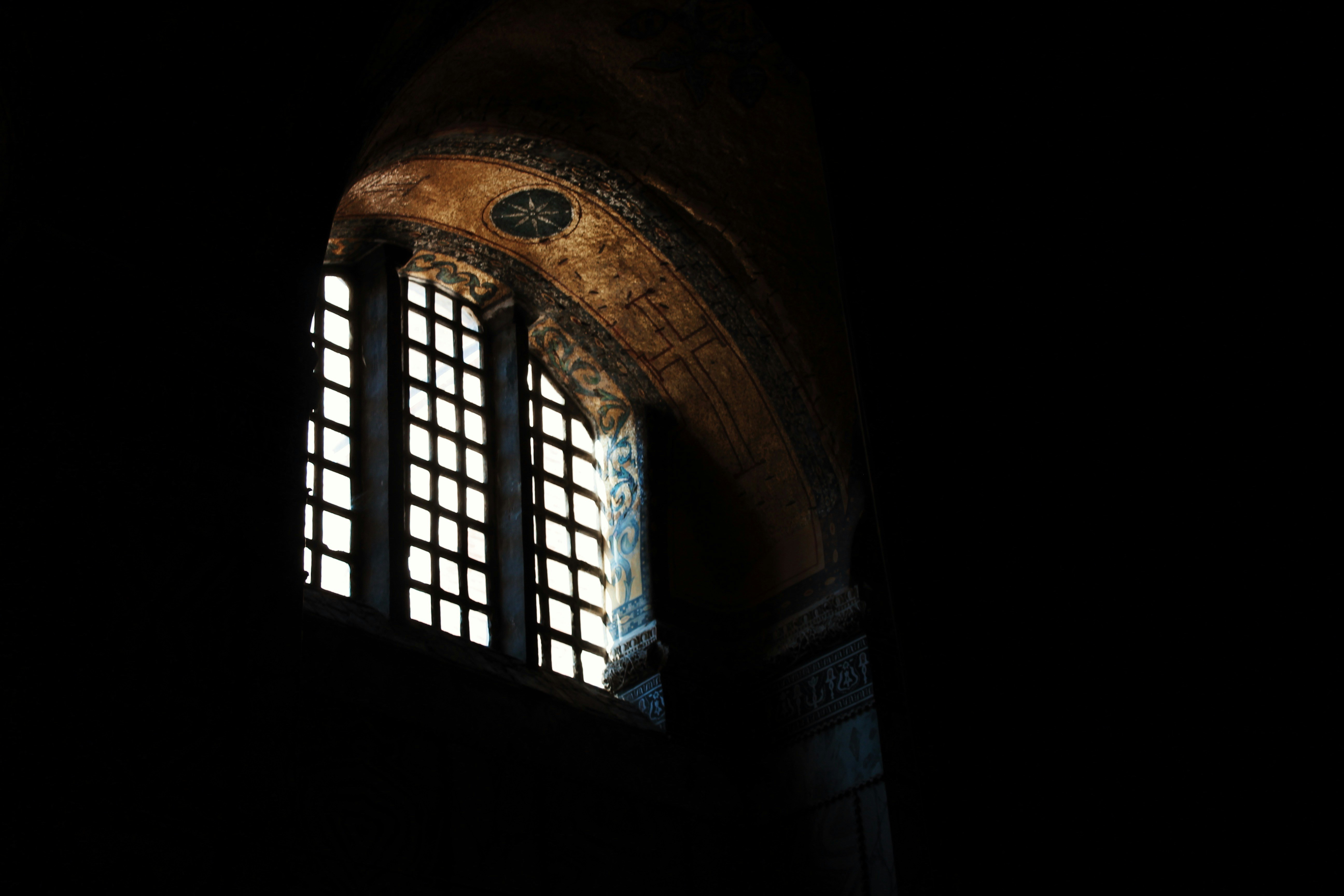 Arched window with intricate lattice casting light into a dim interior.