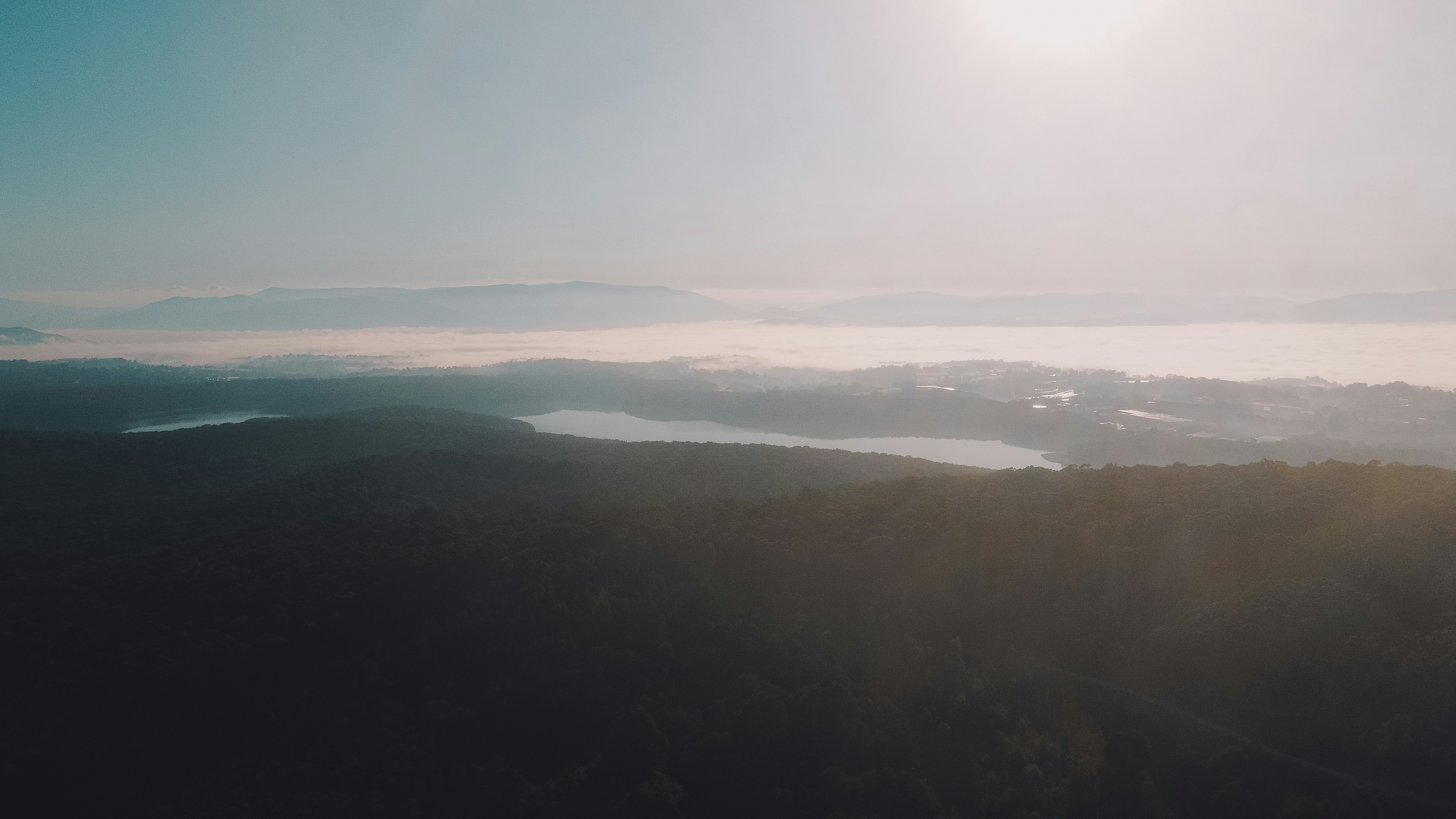 Sunrise view of misty hills partially covered by a blanket of clouds.