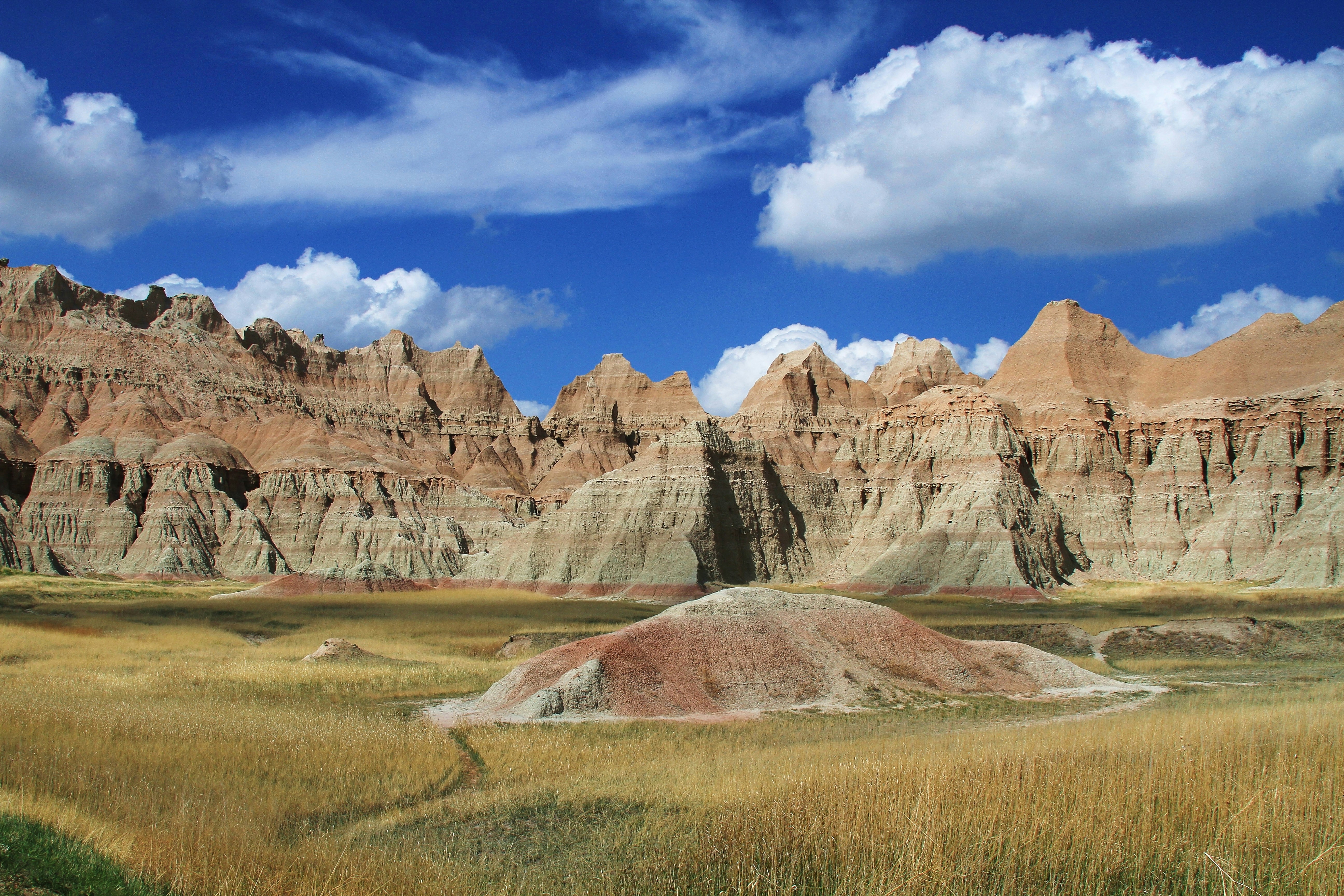 Vast expanse of the Badlands showcasing layered rock formations and golden grasses under a vibrant blue sky with fluffy clouds.