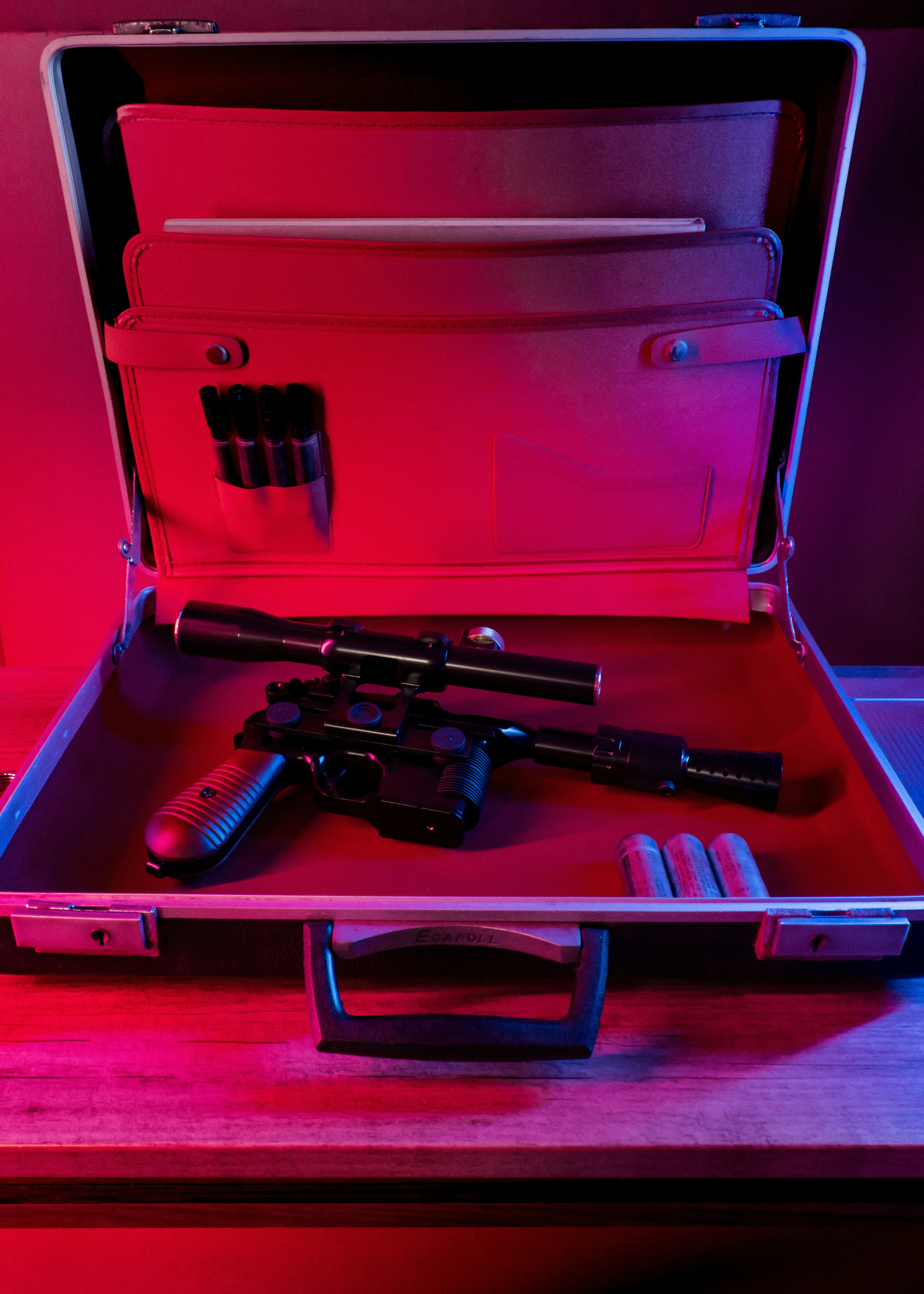A sleek black firearm with a silencer rests inside a metallic briefcase, surrounded by organized tools and cartridges, evoking a sense of intrigue and secrecy.