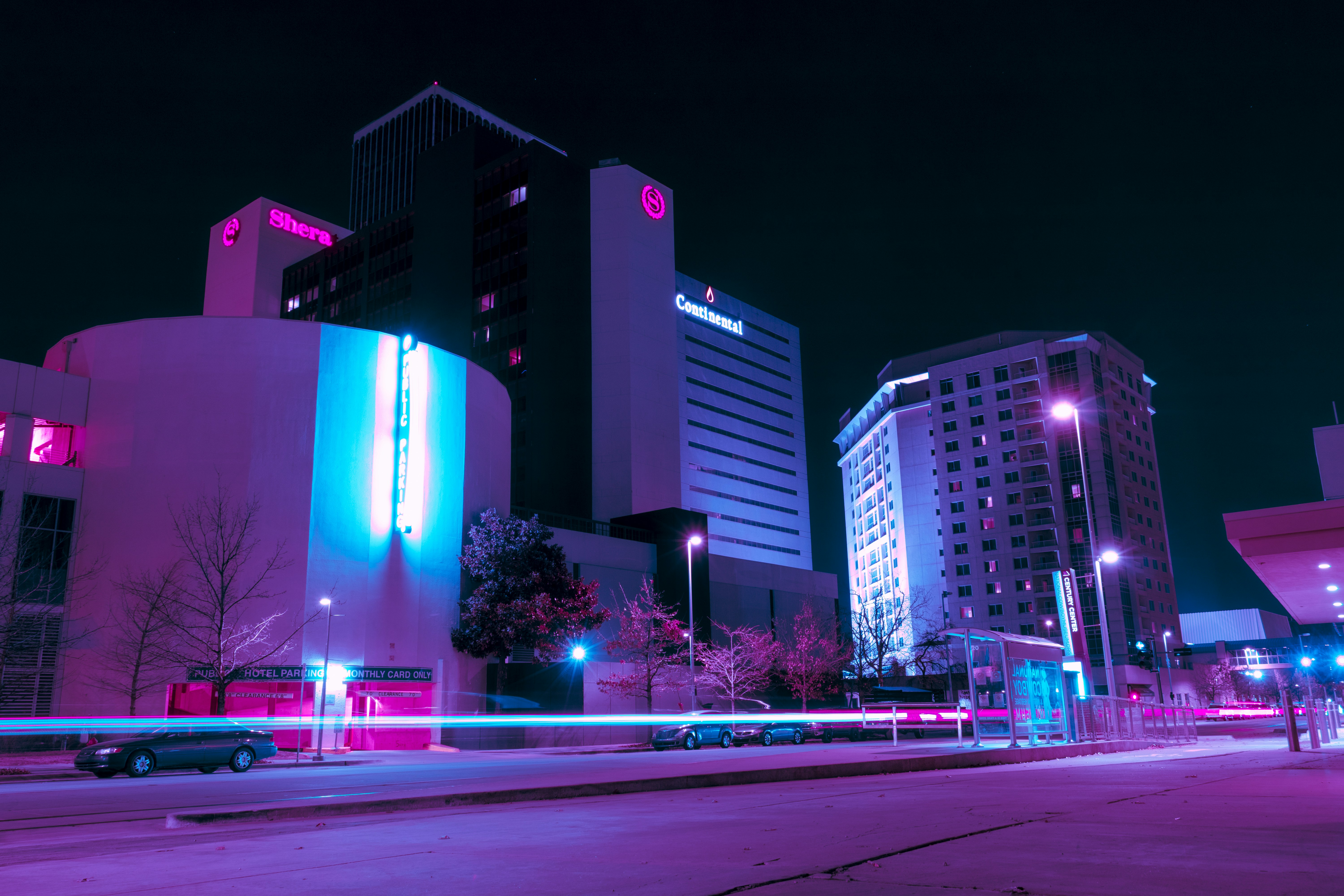 City buildings illuminated by vibrant blue and pink neon lights at night.