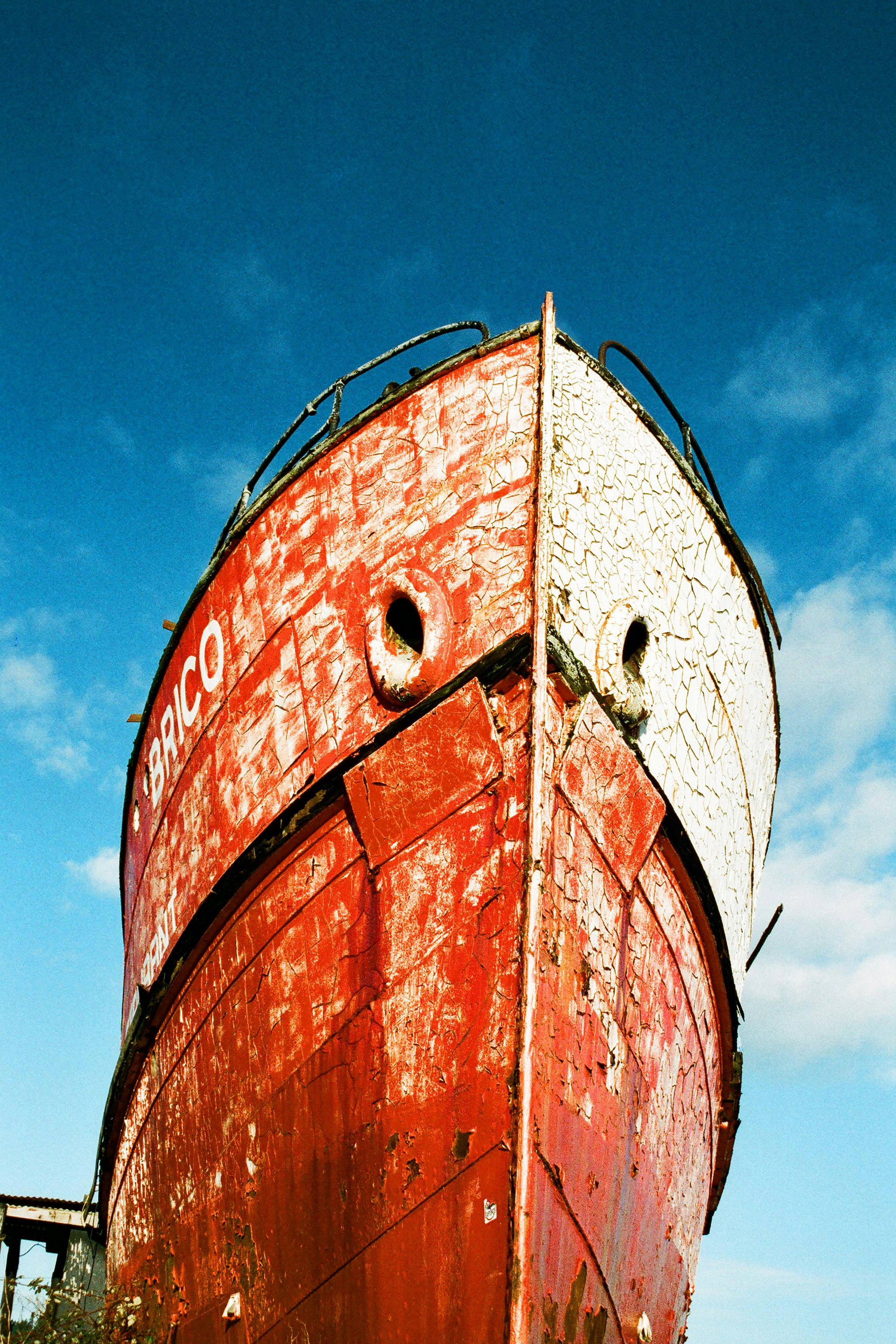 Weathered red boat hull rises against a bright blue sky in a single-shot photograph.