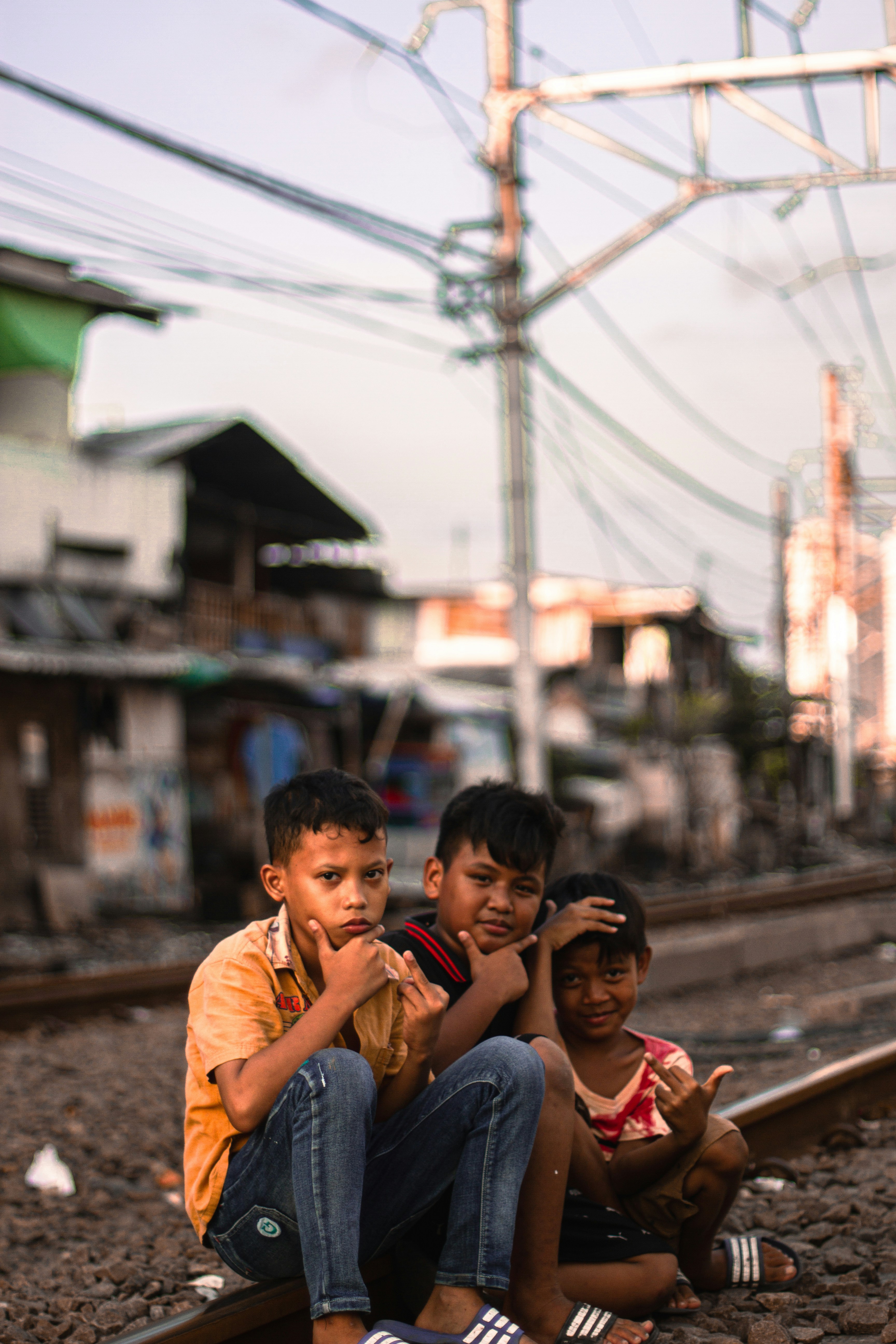 Three boys sitting on railway tracks, expressing camaraderie and playfulness against a backdrop of urban structures and power lines.