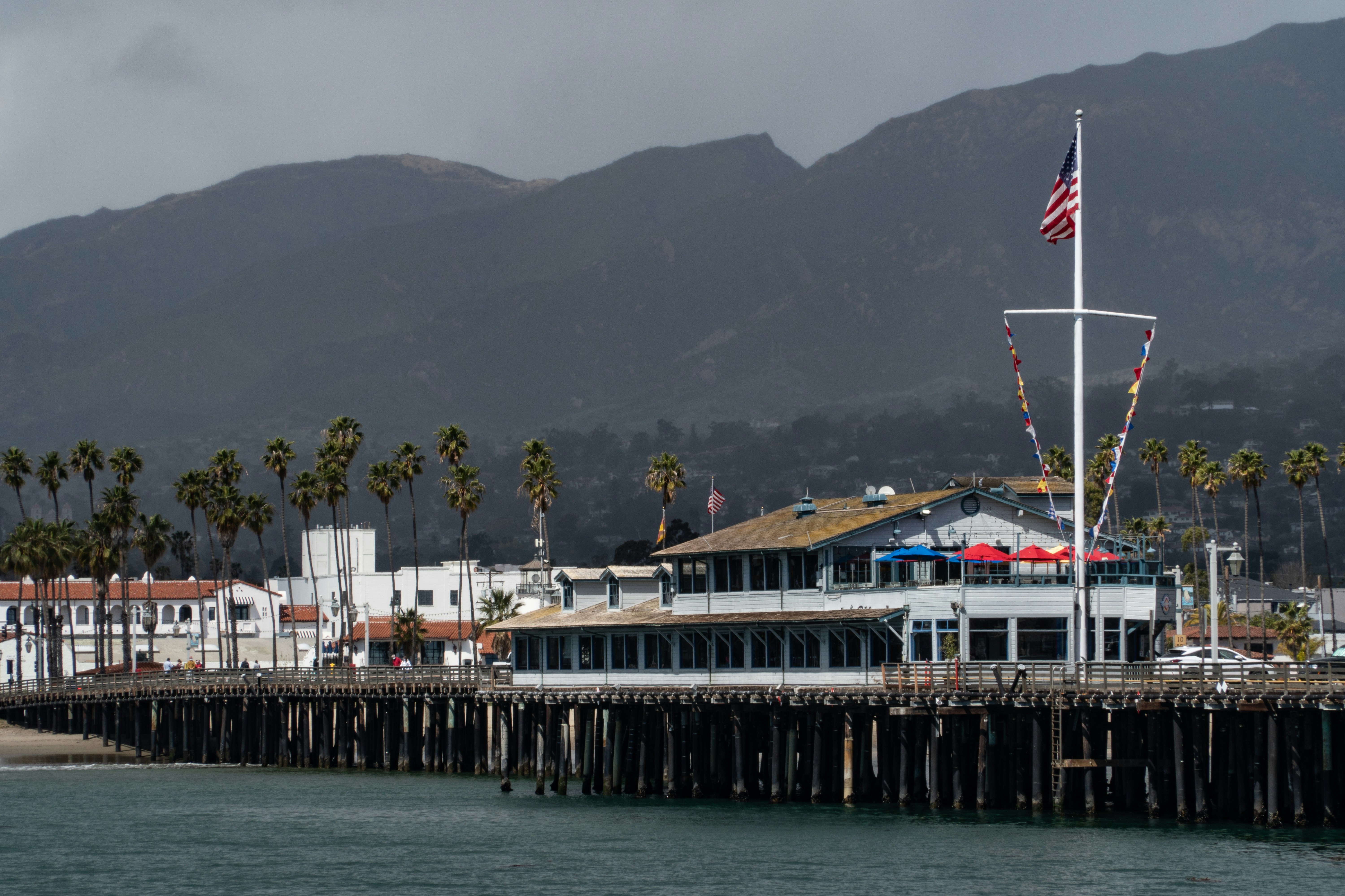 Flagpole over the Pier: Palm-Lined Horizon and Mountain Backdrop