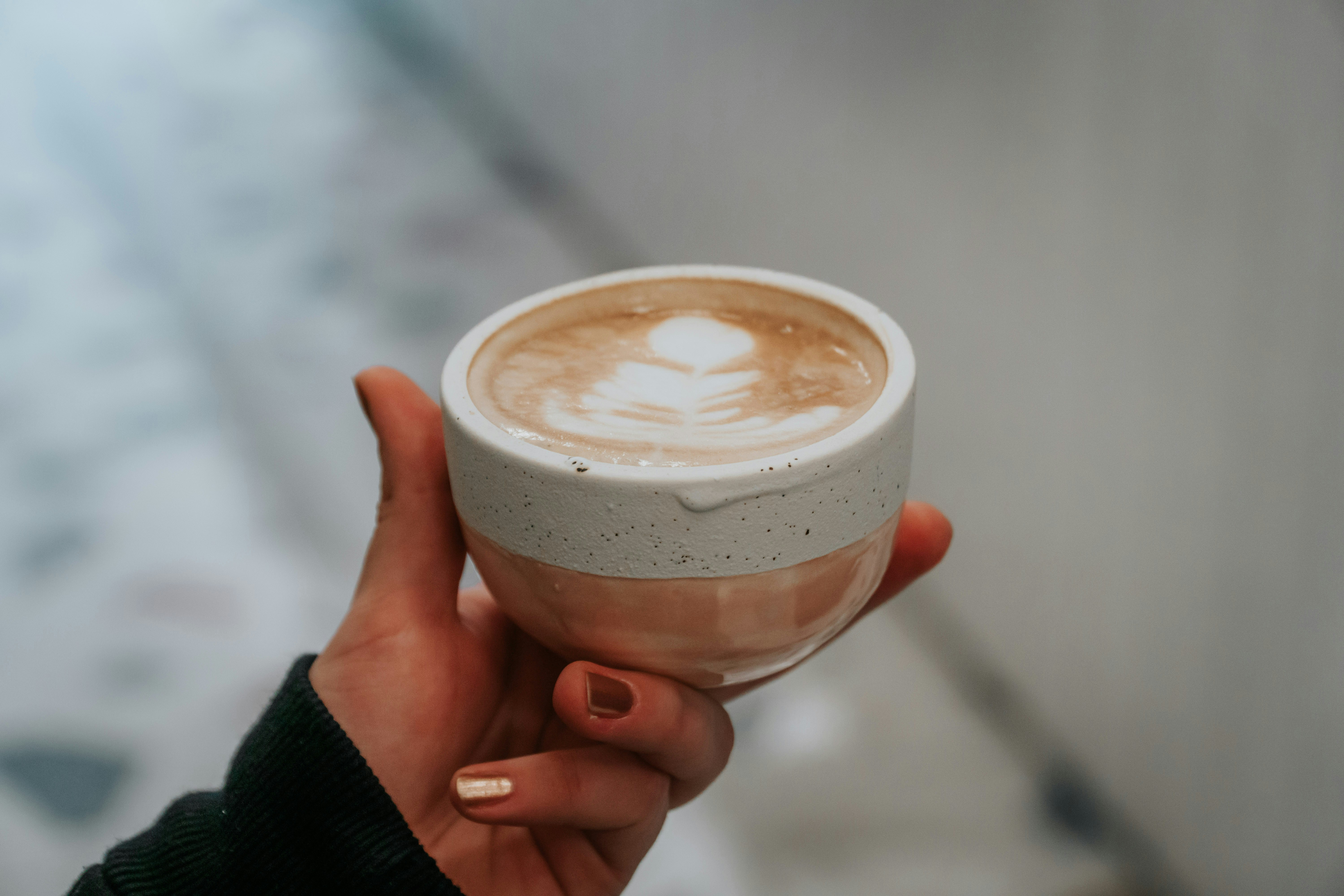 person holding white ceramic mug with brown liquid