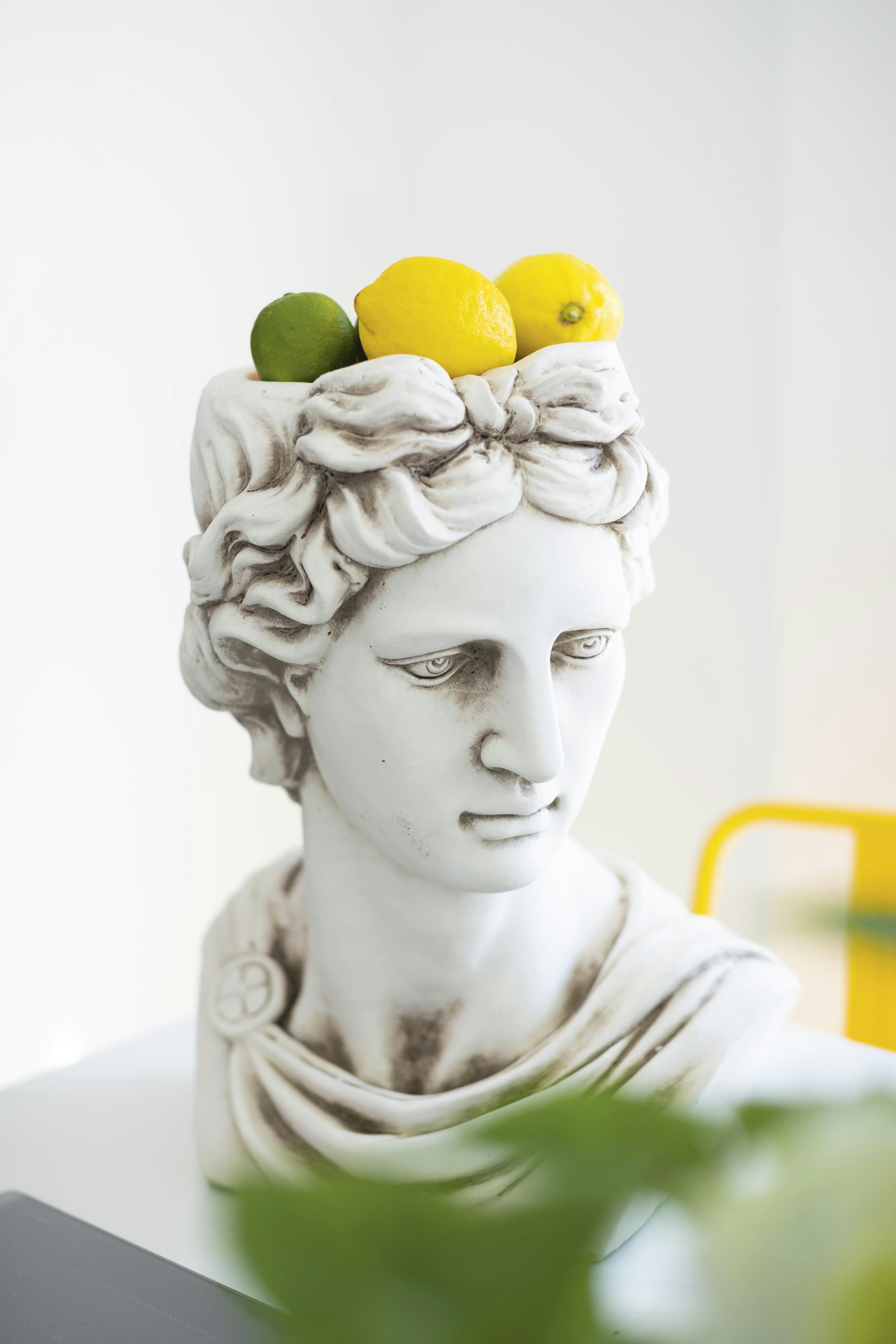 A marble bust adorned with fresh lemons and limes, blending classical art with modern fruit display.
