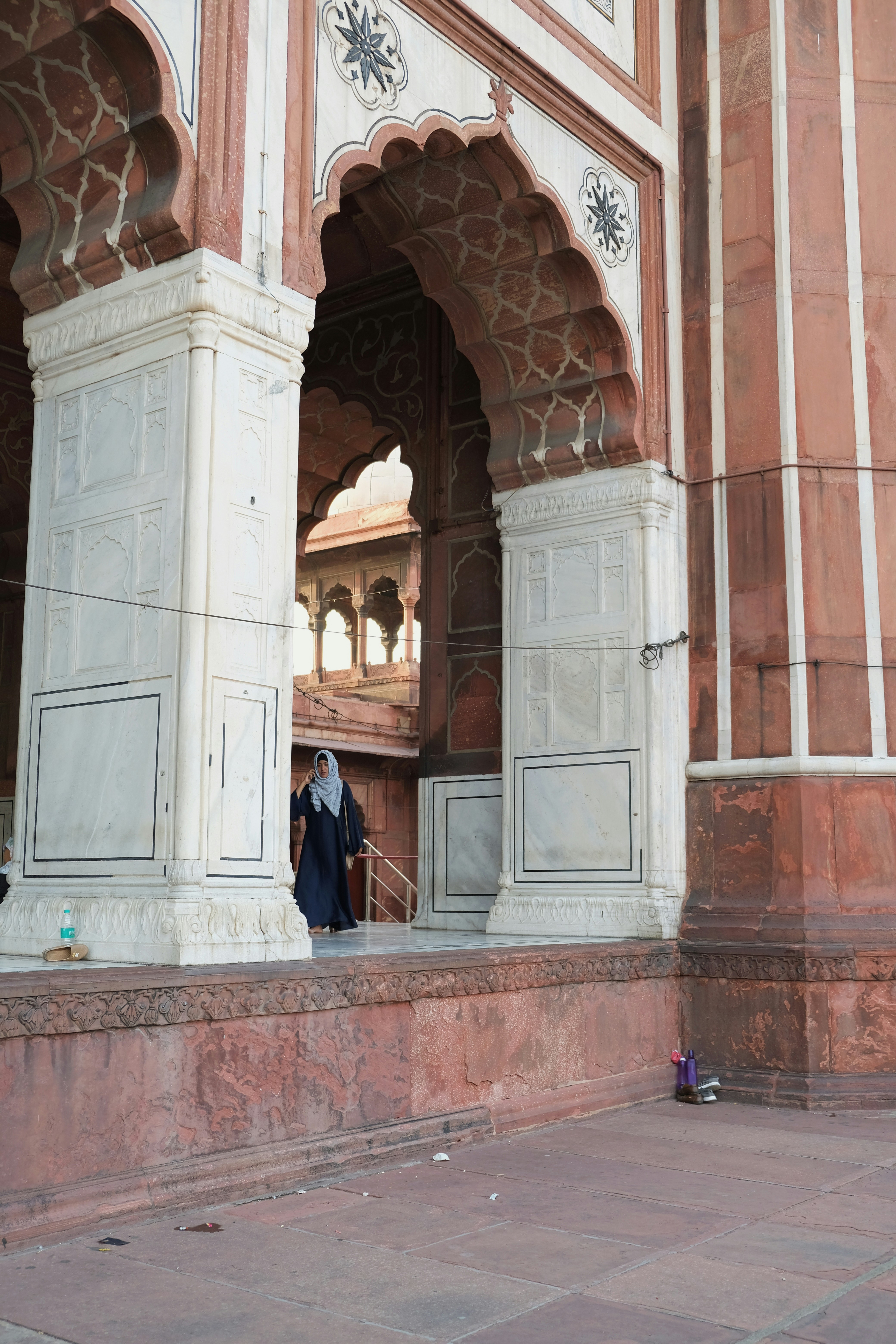 Person in a blue jacket walks through the ornate archway of Jama Masjid in Delhi.