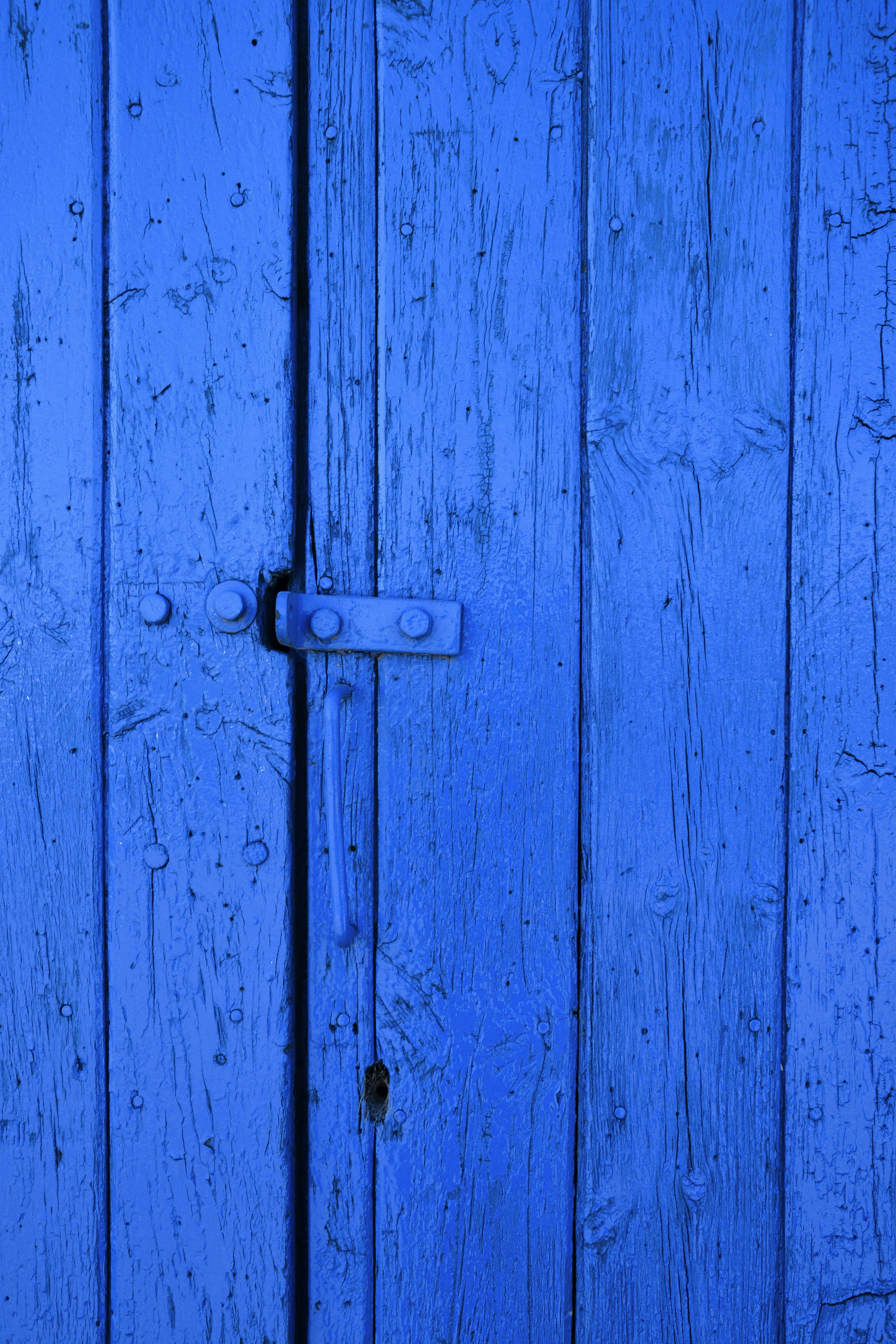 Vibrant blue wooden door with a rustic latch, showcasing texture and character. The deep color highlights the natural grain and imperfections of the wood.