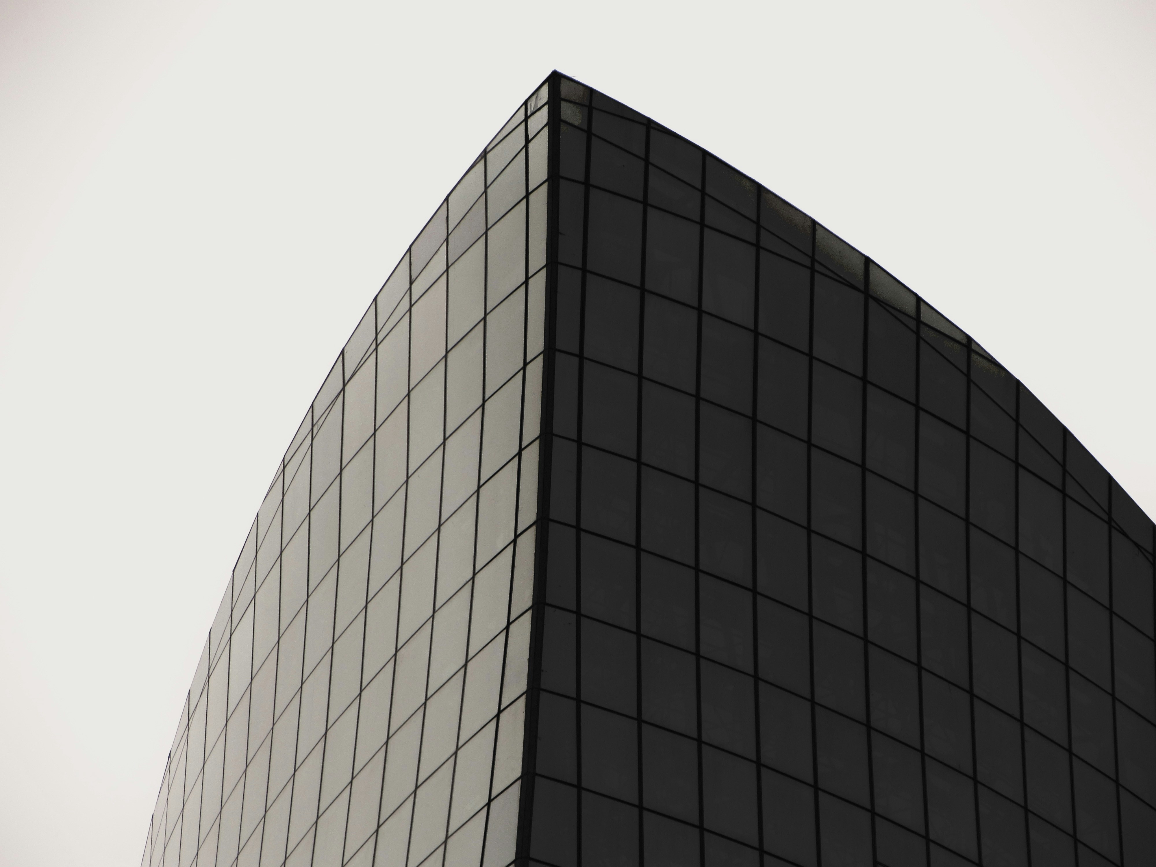 Sharp architectural corner of a glass building reflecting muted light against a pale sky.