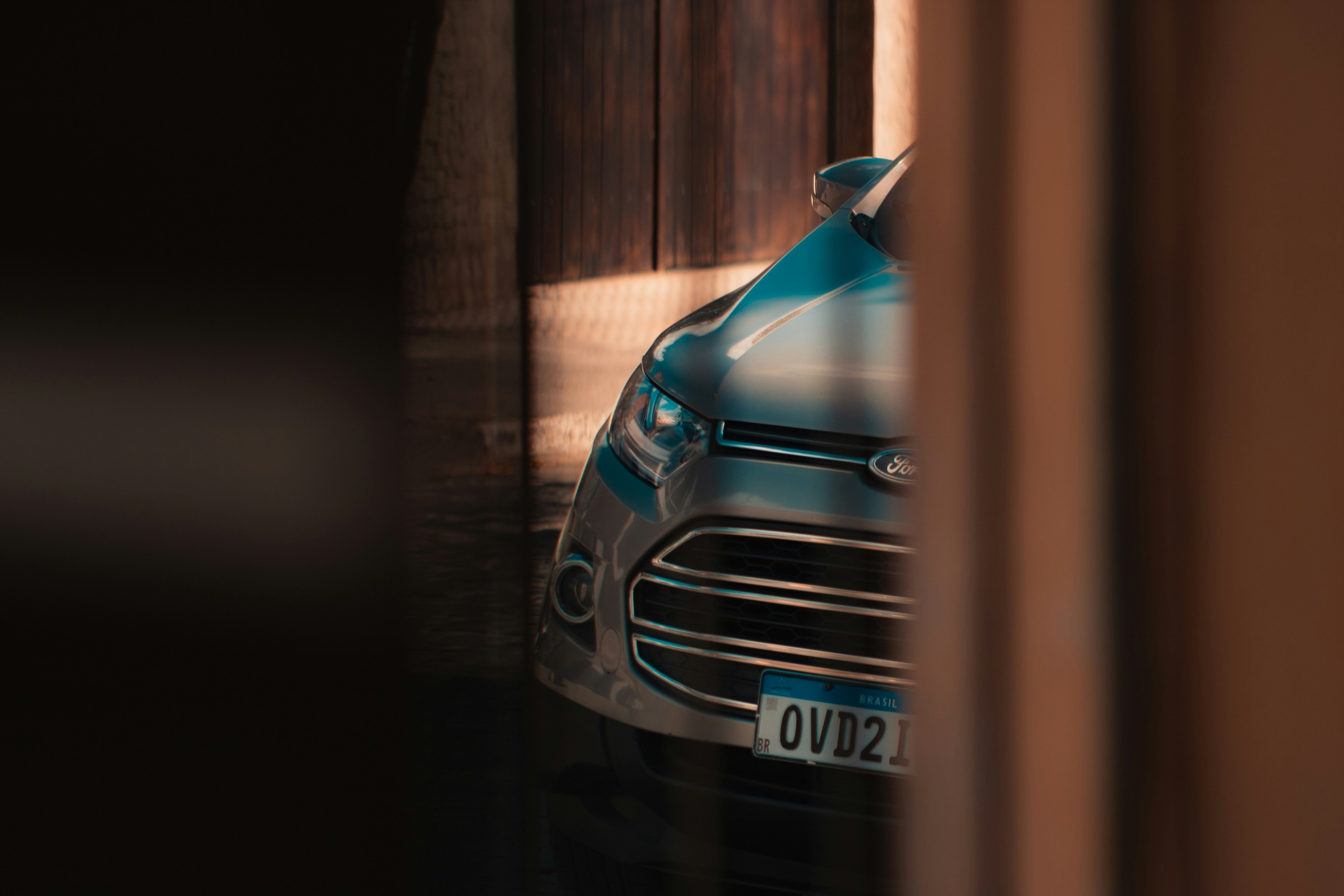 A Ford vehicle partially obscured by a wooden structure, highlighting its sleek design and reflective surfaces.