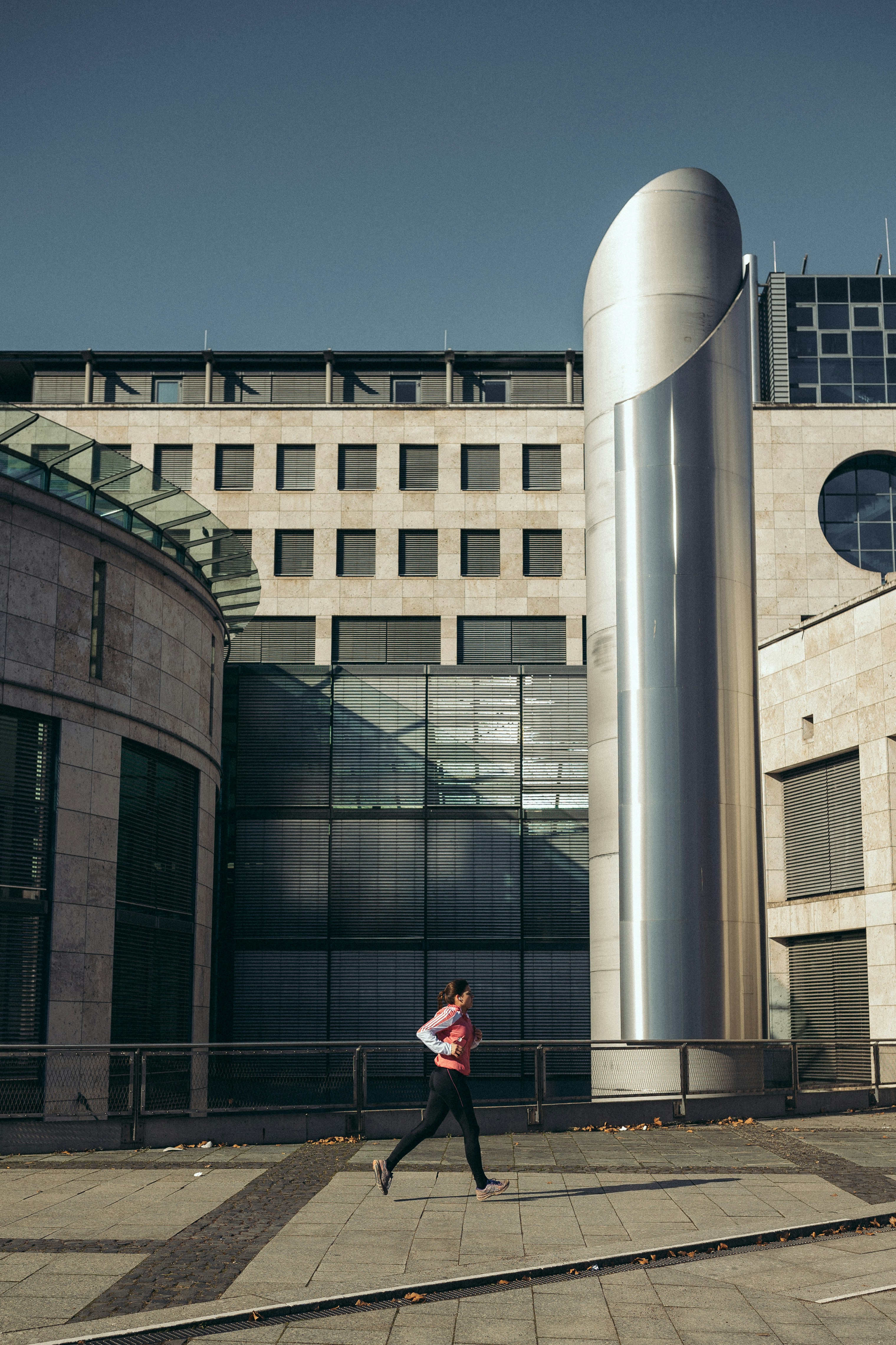 A runner in athletic gear moves briskly past sleek, contemporary architecture, showcasing the harmony between human activity and urban design.