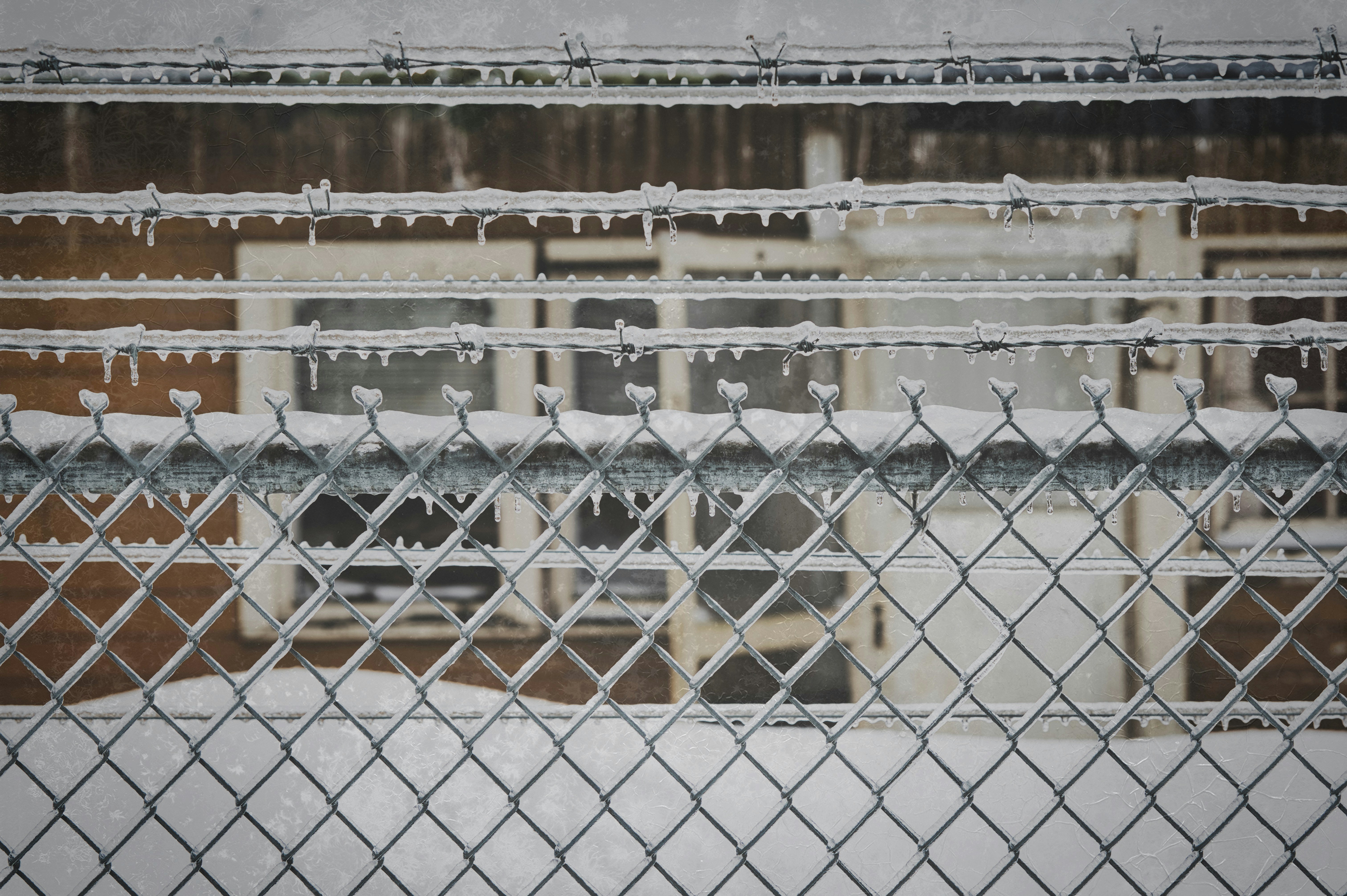 Fence will thick ice with a snowy covered building in the back.
