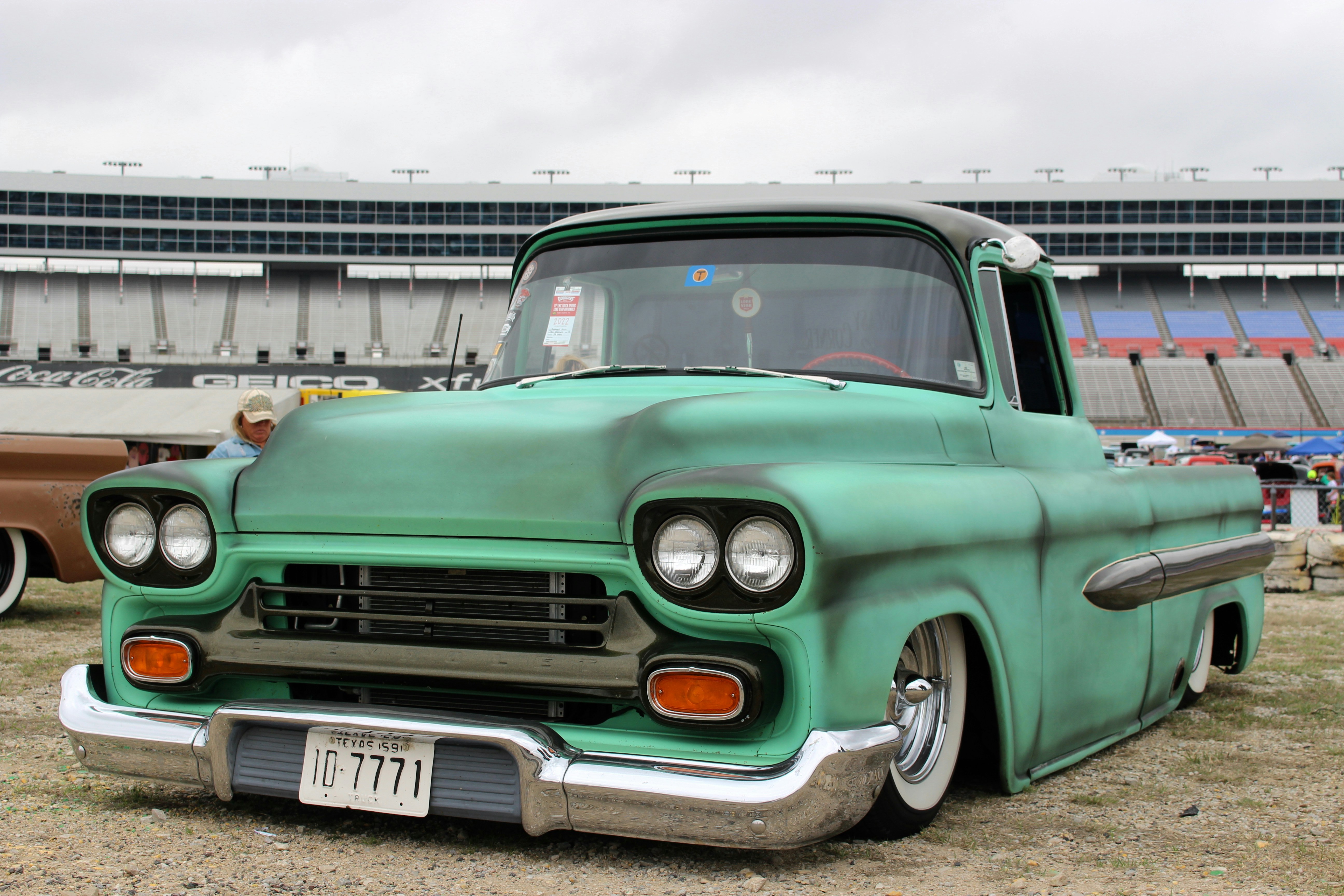 Retro green pickup truck parked on grass with a racetrack in the background.