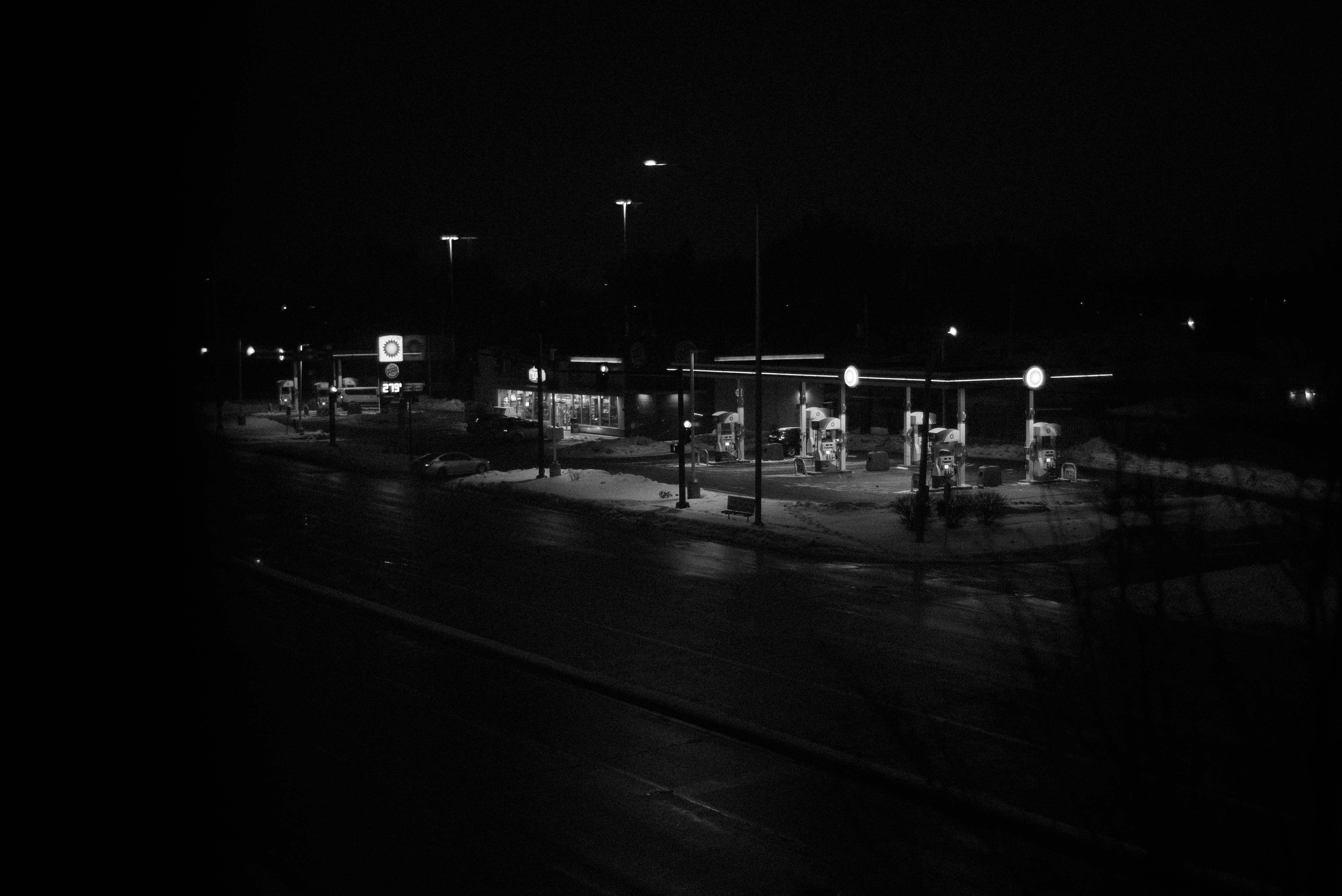 A gas station illuminated under the night sky, showcasing empty forecourts and glistening wet asphalt.