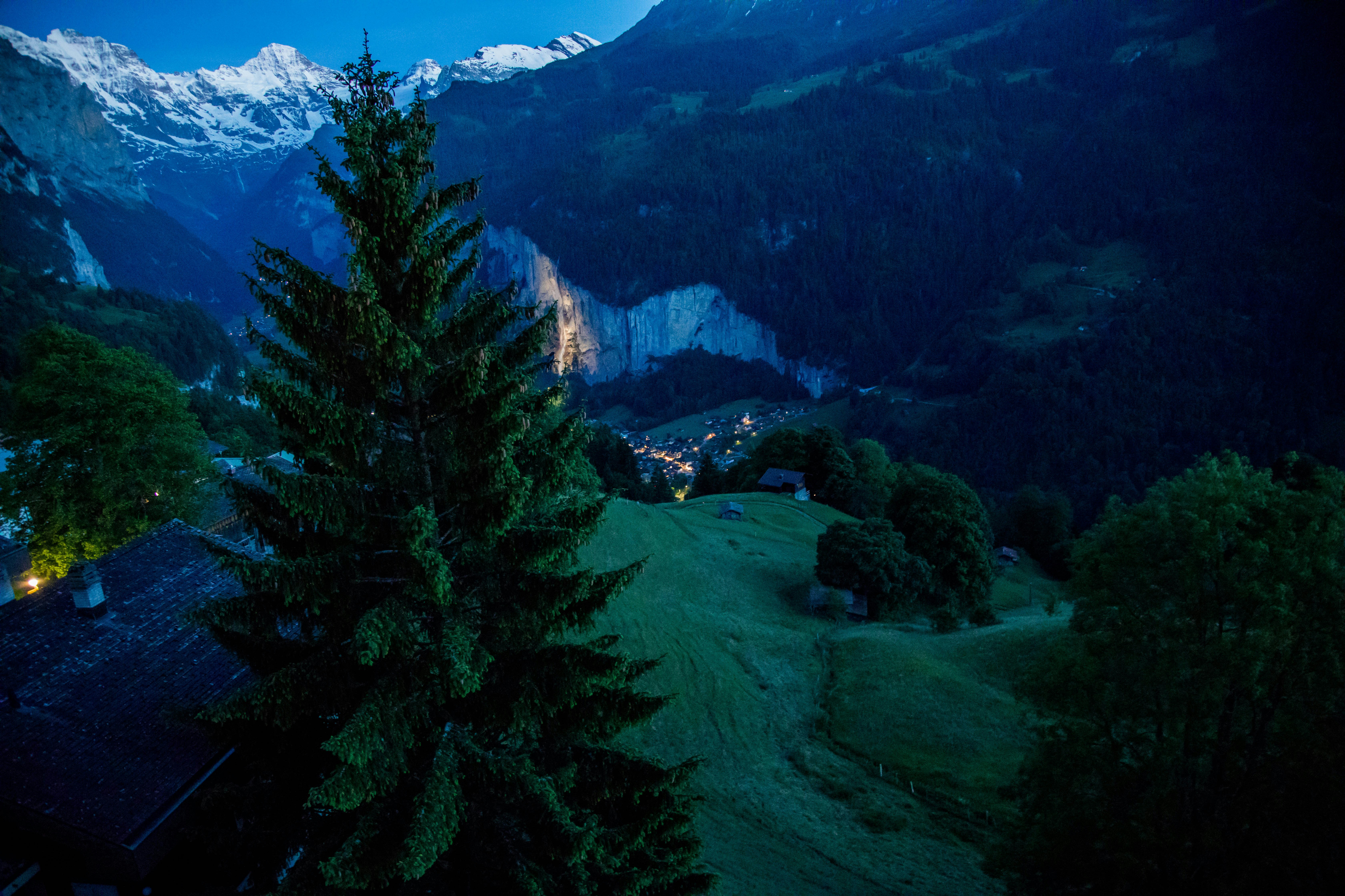 A serene alpine landscape at twilight, featuring a lush green valley and distant mountain peaks illuminated by the fading light. The scene captures the tranquil beauty of nature.