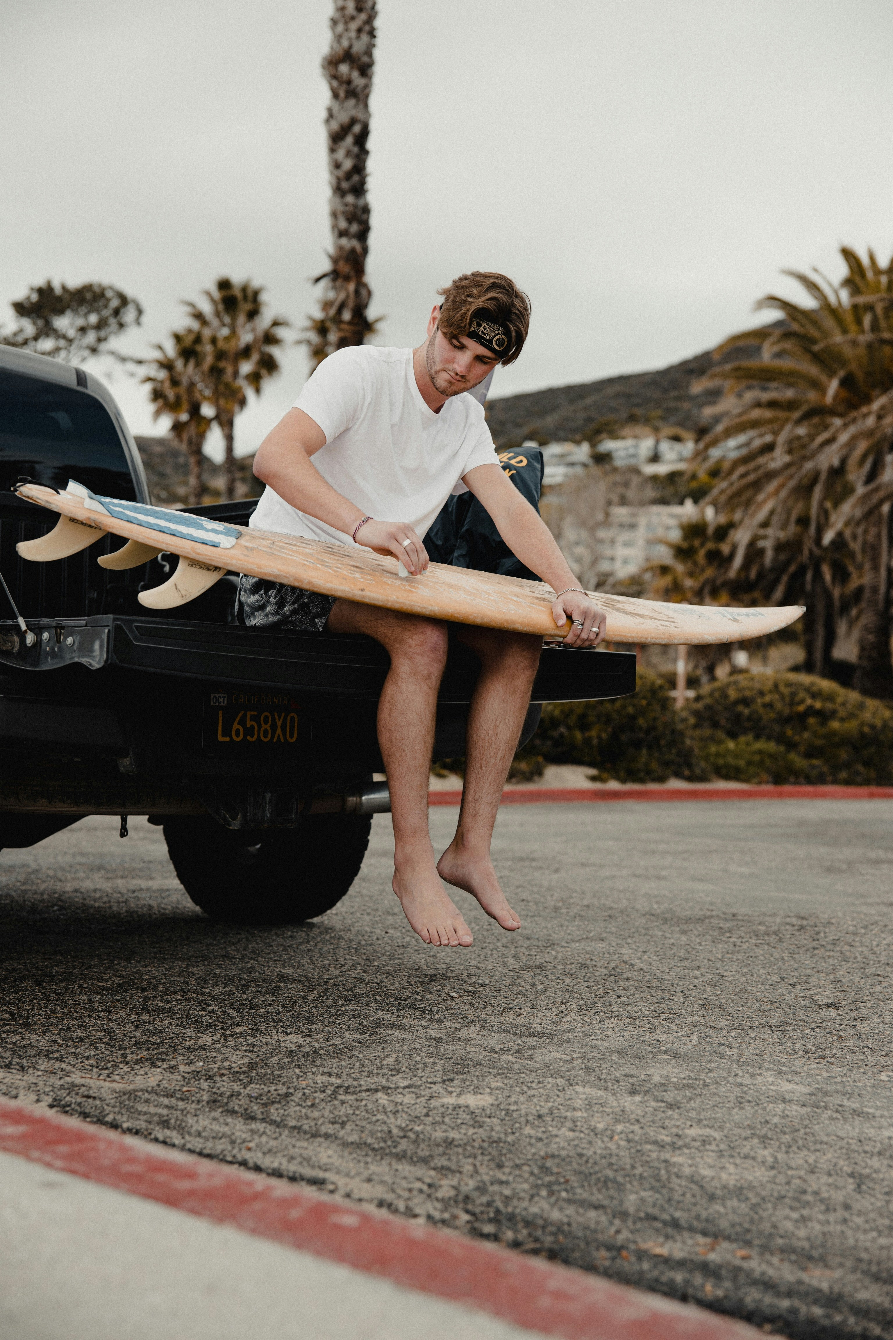 Hitching a Surf Session: A Lone Surfer Pauses in a Coastal Parking Lot