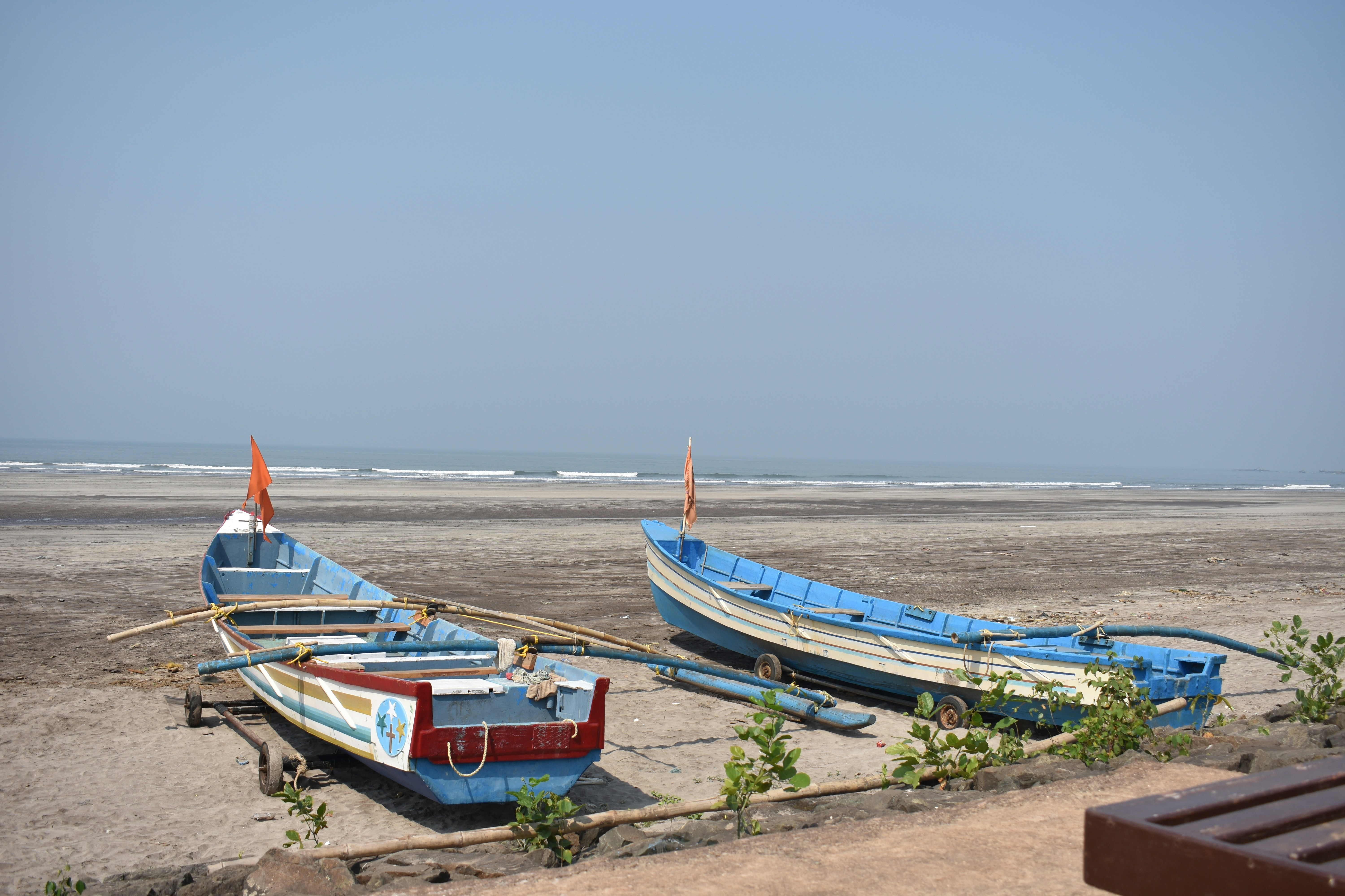 Two colorful fishing boats rest on a sandy beach, their vibrant hues contrasting with the muted landscape as the tide recedes.
