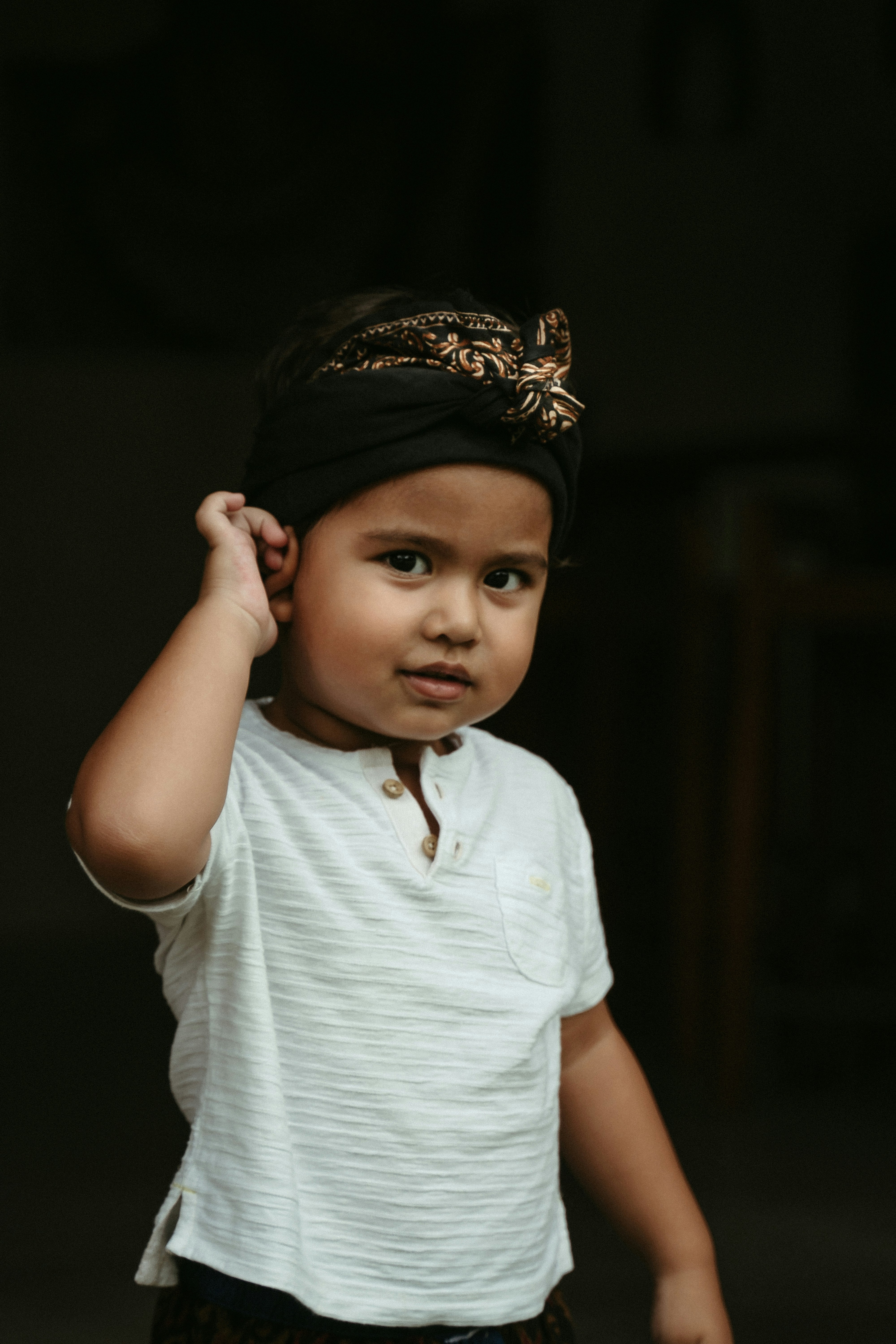 Child with Turban: Quiet Confidence in a Dim Studio