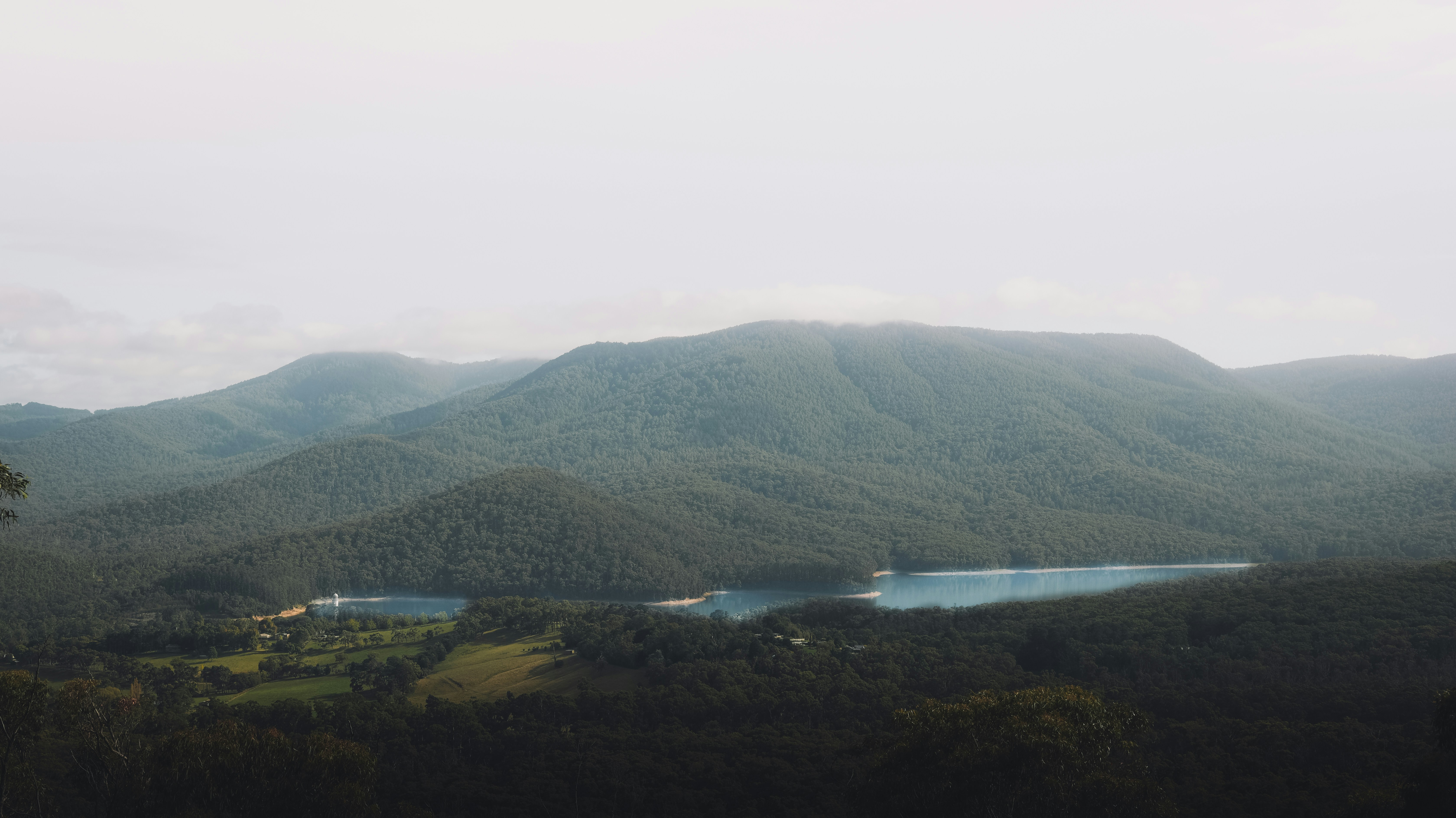 Lush green mountains surrounding a tranquil body of water under a cloudy sky.