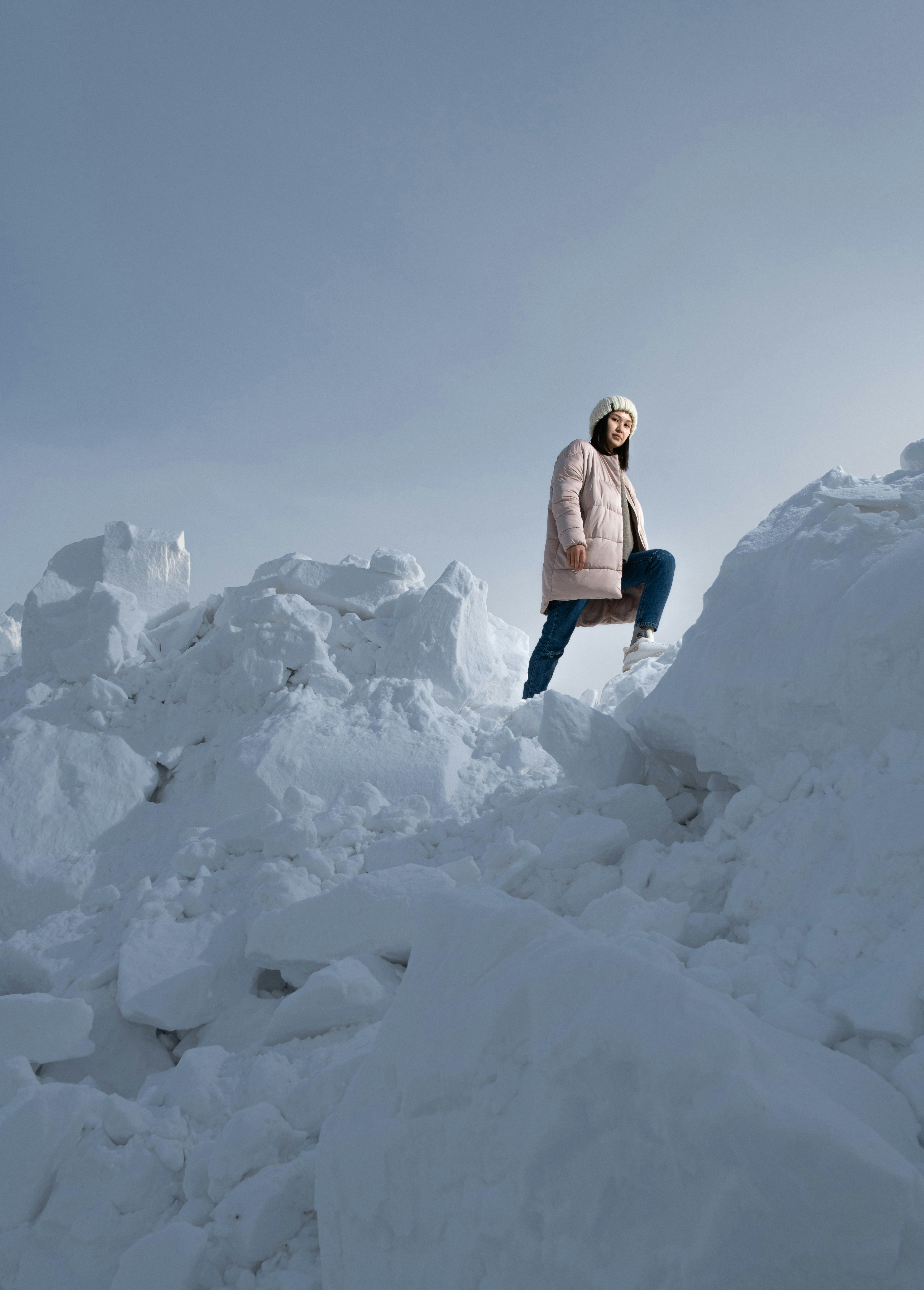 Pastel Parka on a Frost Crest: A solitary climber crowns a snowy ridge under a pale blue sky