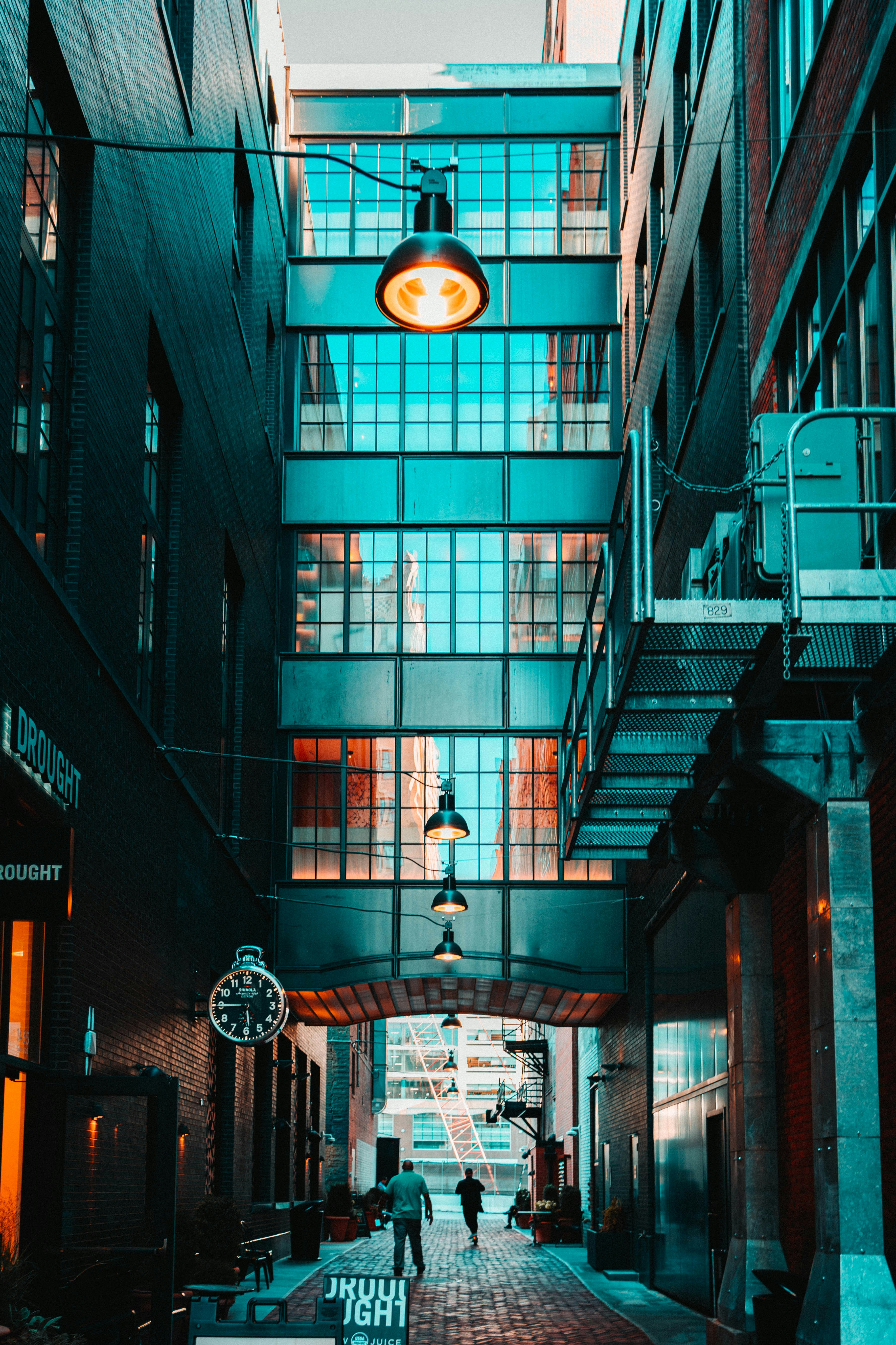 A vibrant alleyway showcasing modern architecture with striking reflections and warm light, leading to a distant figure. The scene highlights the contrast between the old and new urban elements.