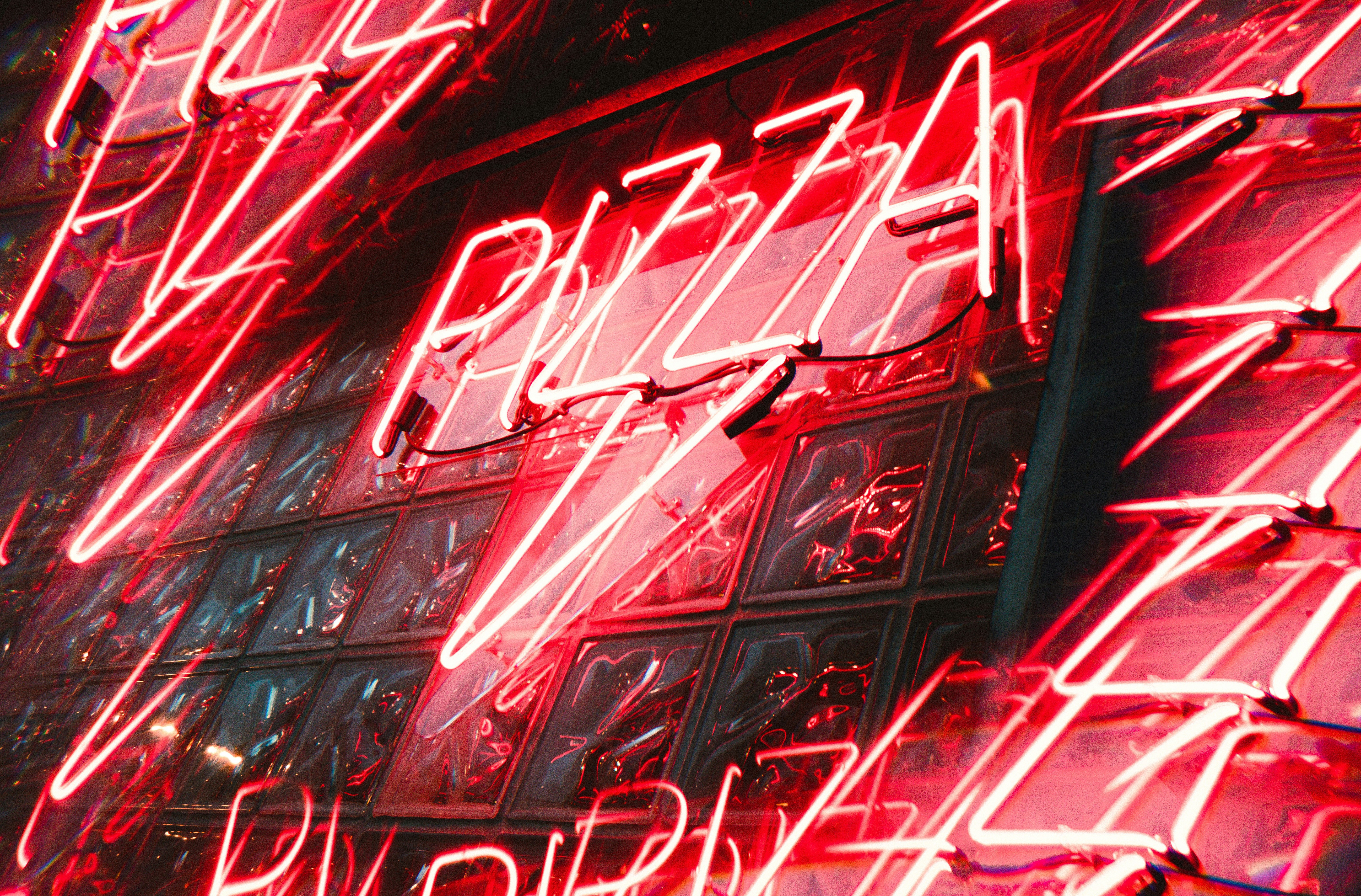 Vibrant neon signage advertising pizza, with striking red hues illuminating the surrounding area.