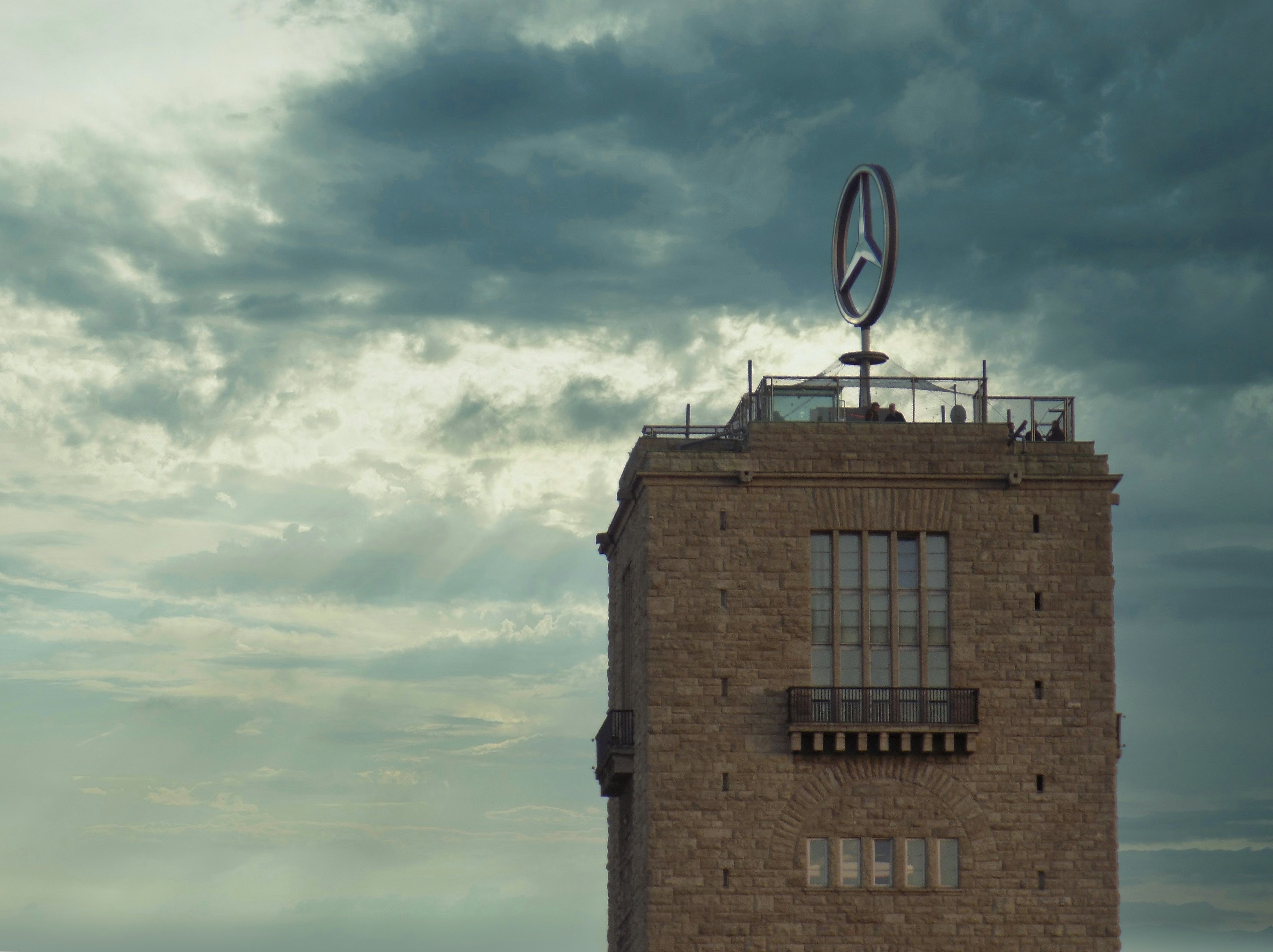 Brown concrete tower with a Mercedes-Benz emblem against a dramatic cloudy sky.