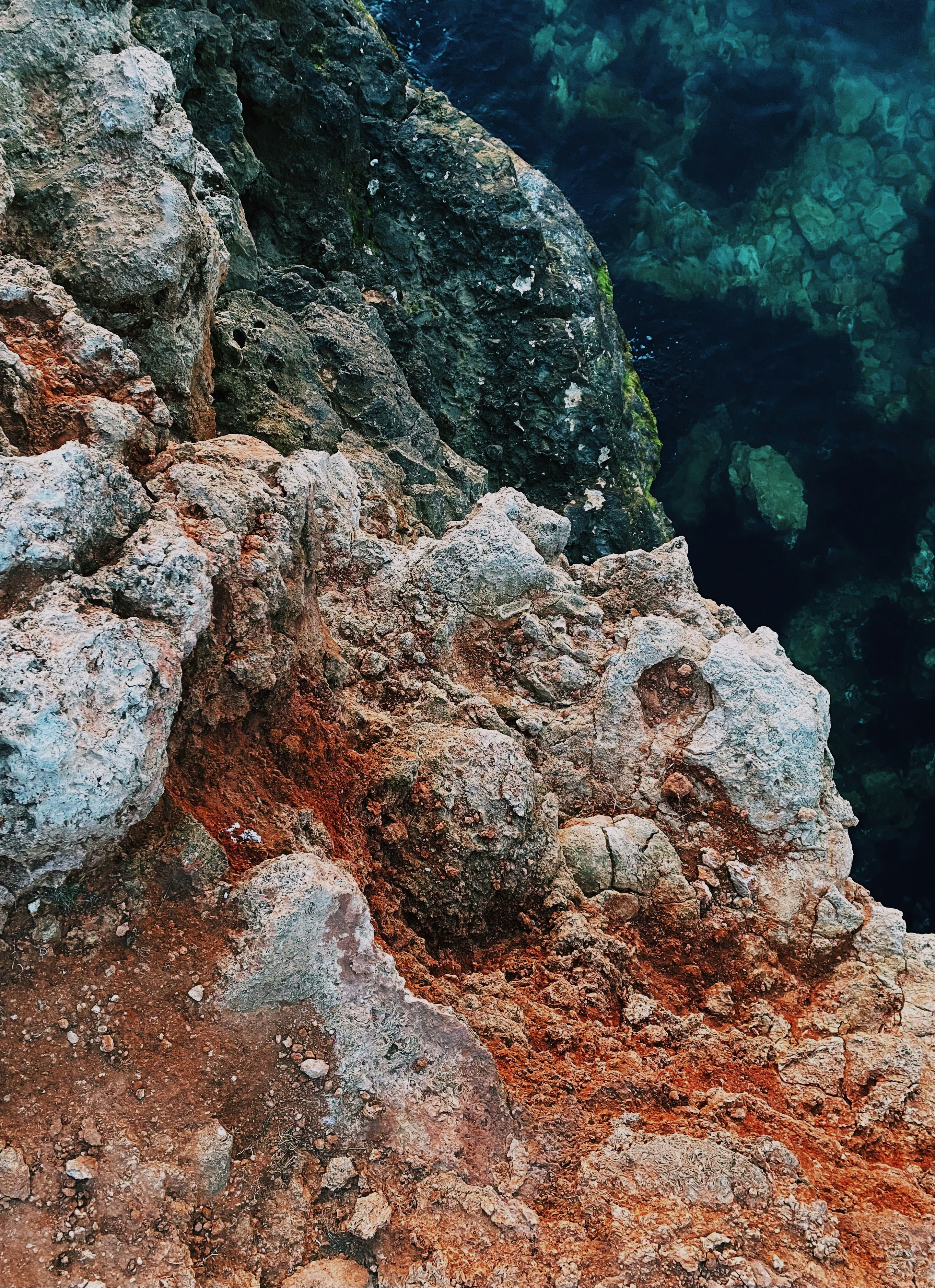 Rugged cliffside with textured rocks meeting deep, clear waters below, showcasing the natural beauty of coastal geology.