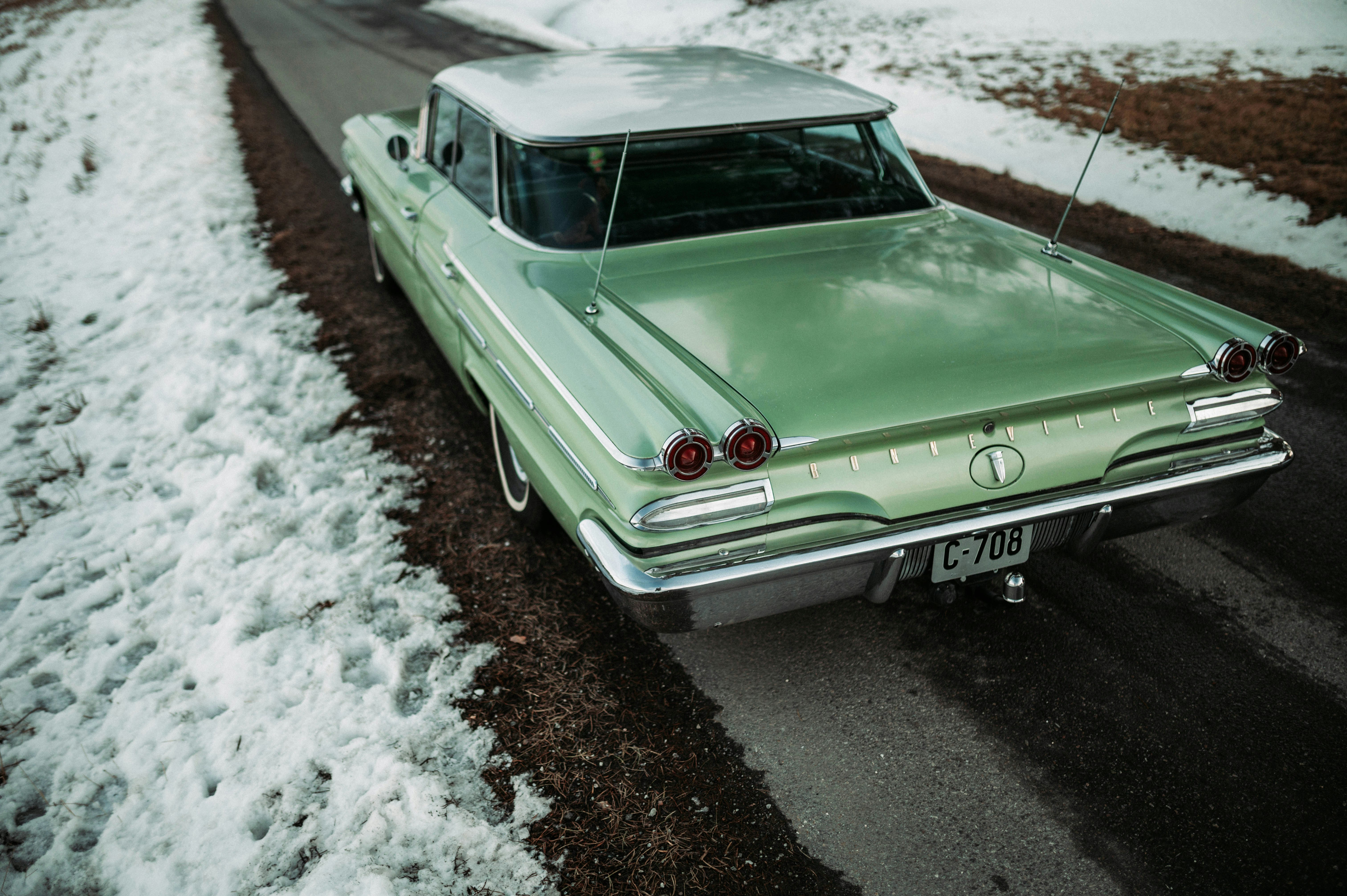 Vintage green car parked beside a snowy road, showcasing its retro design against a contrasting winter landscape.