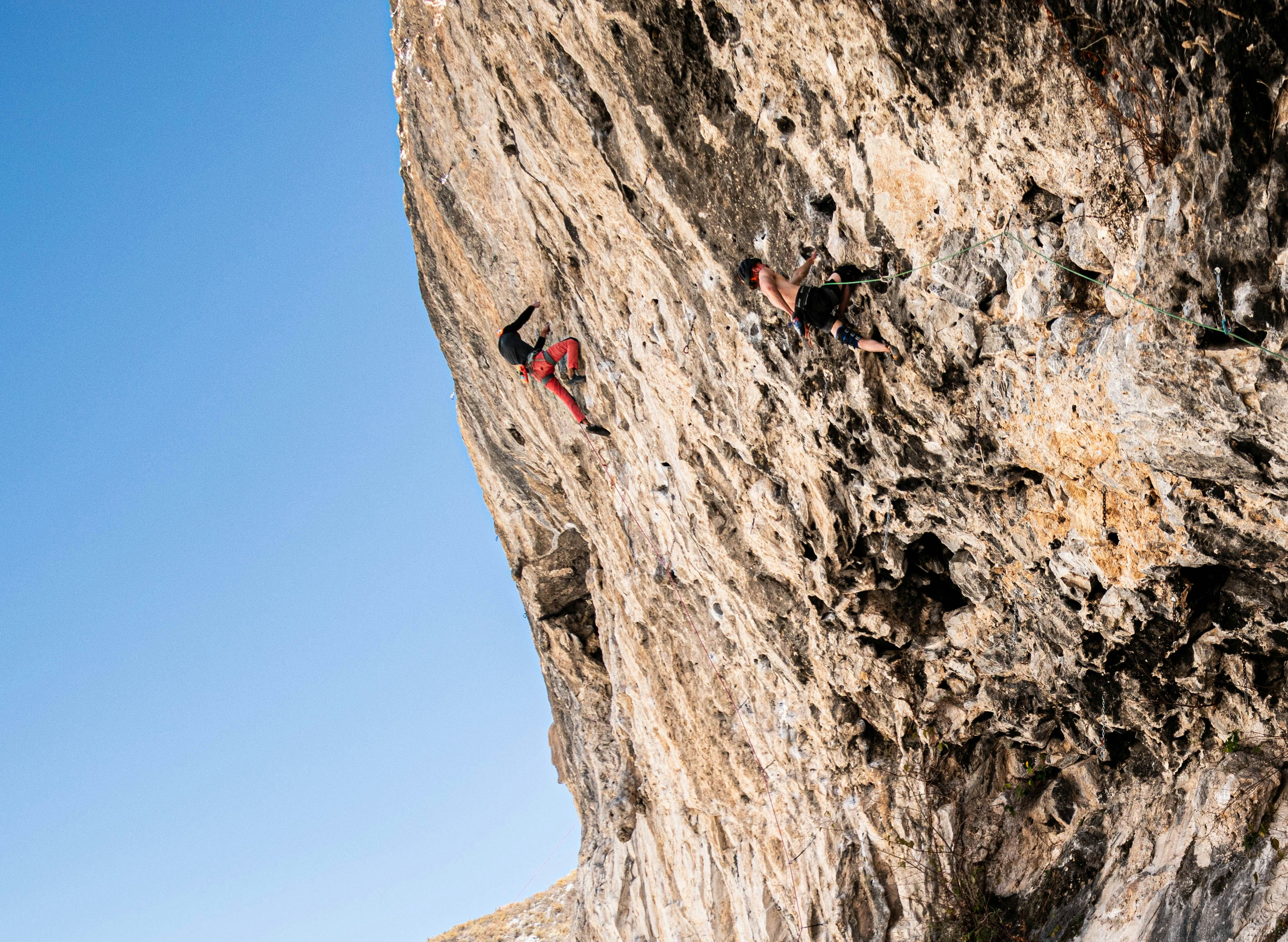 Rock climbers scaling a steep, rugged cliff face under a clear blue sky.