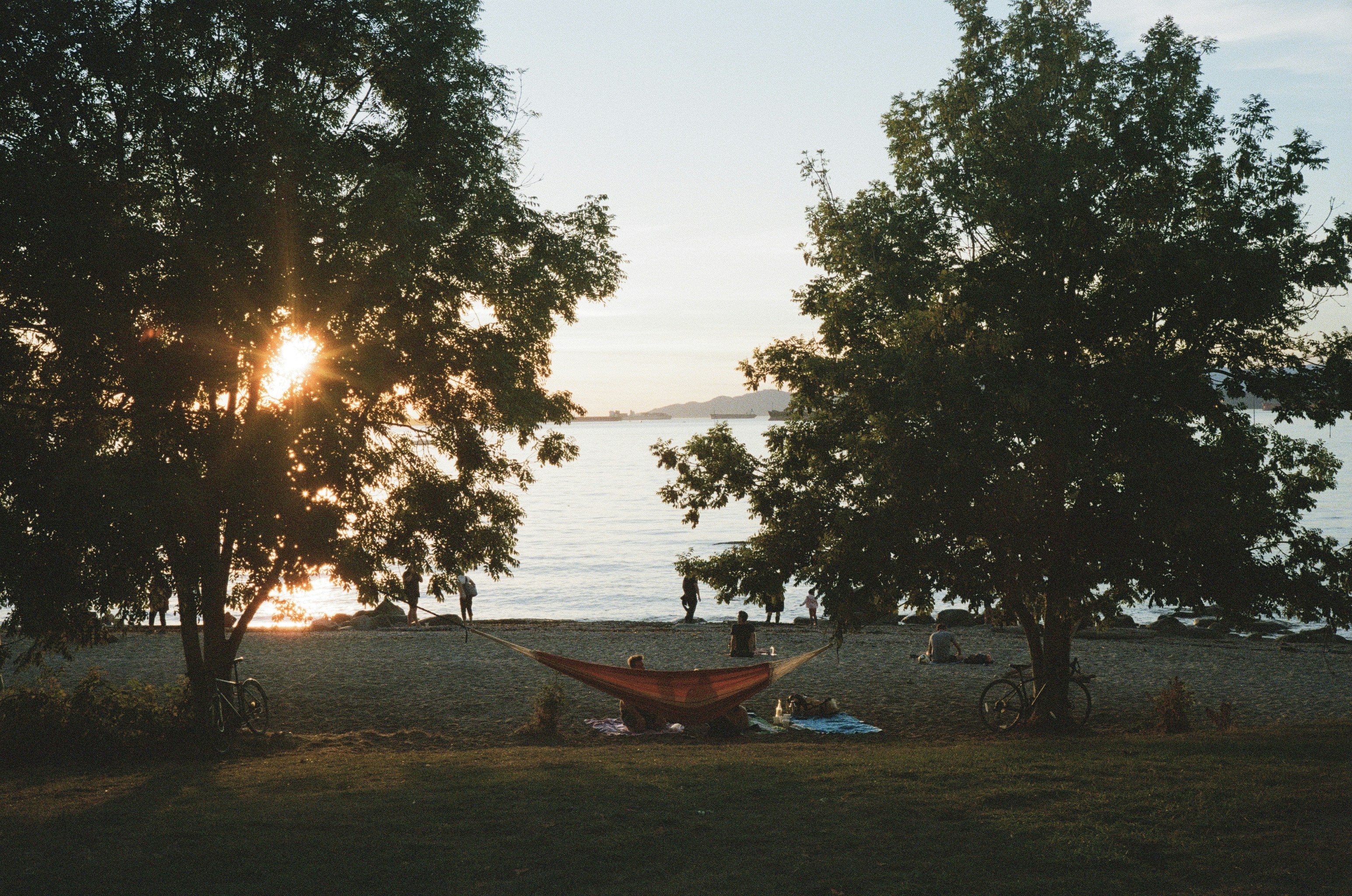 Hammock strung between two trees on a lakeside beach at sunset.