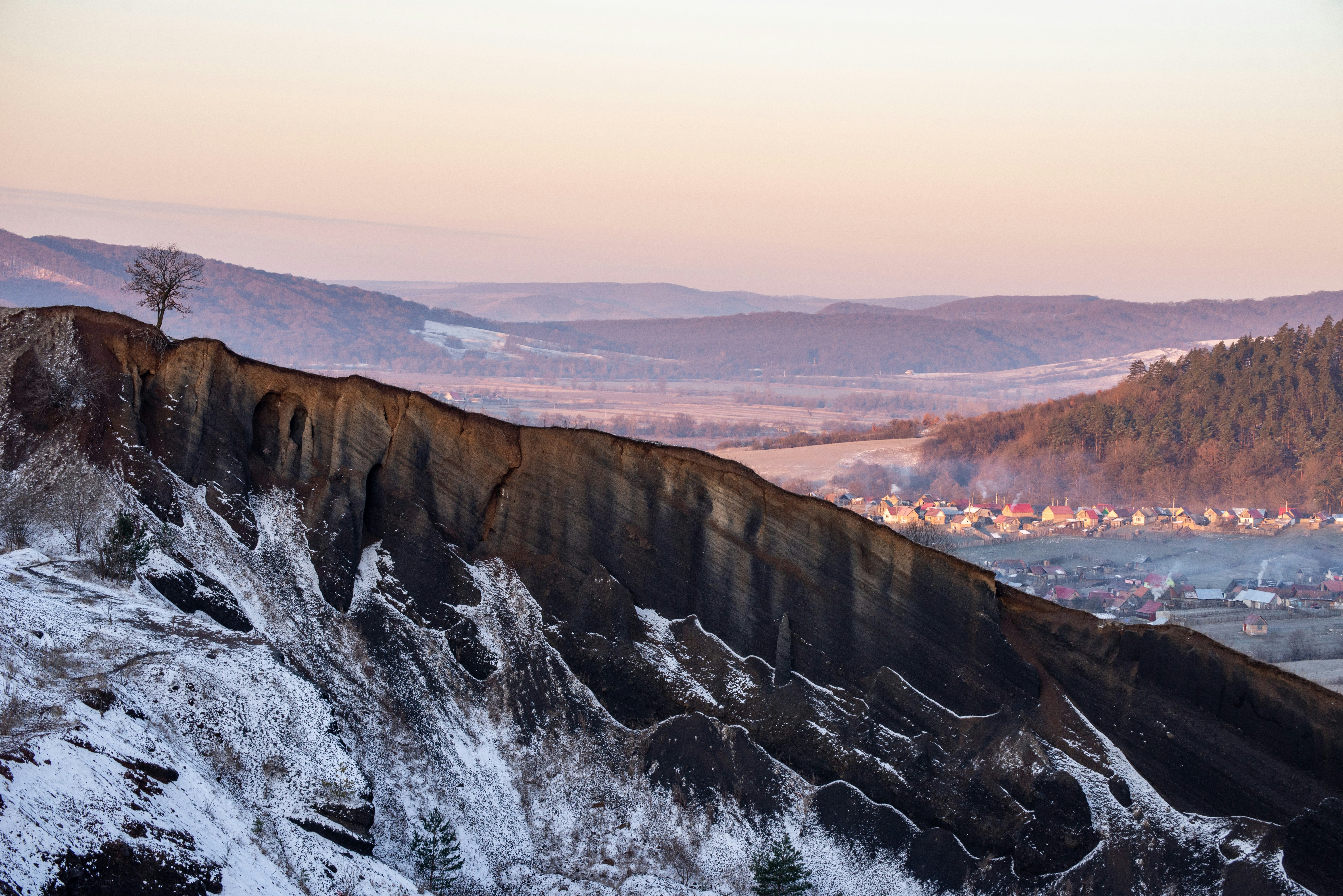Snow-dusted cliffs overlook a valley bathed in the soft hues of dawn.