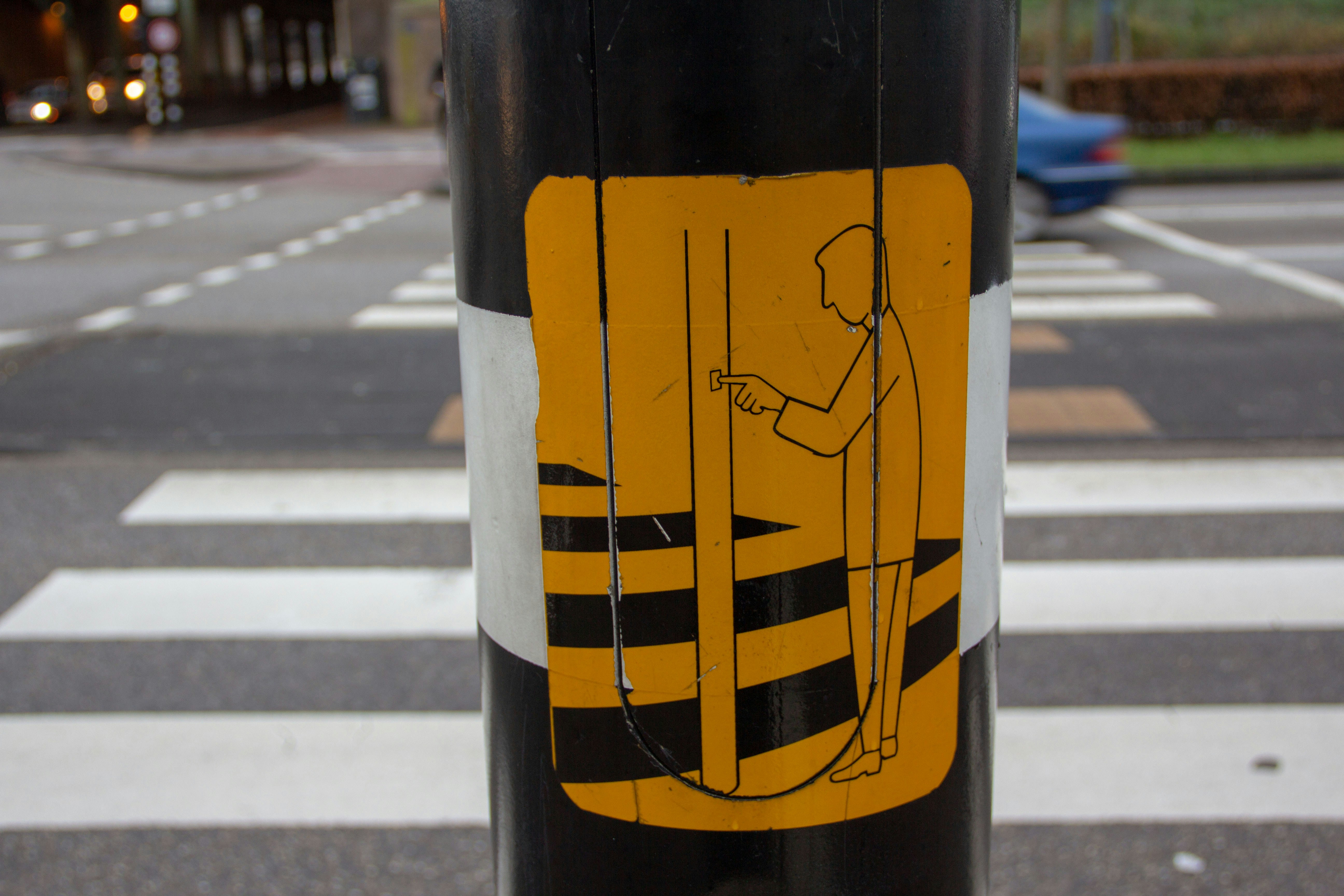 Illustration of a pedestrian signaling device on a traffic pole, depicting a person interacting with the signal mechanism.