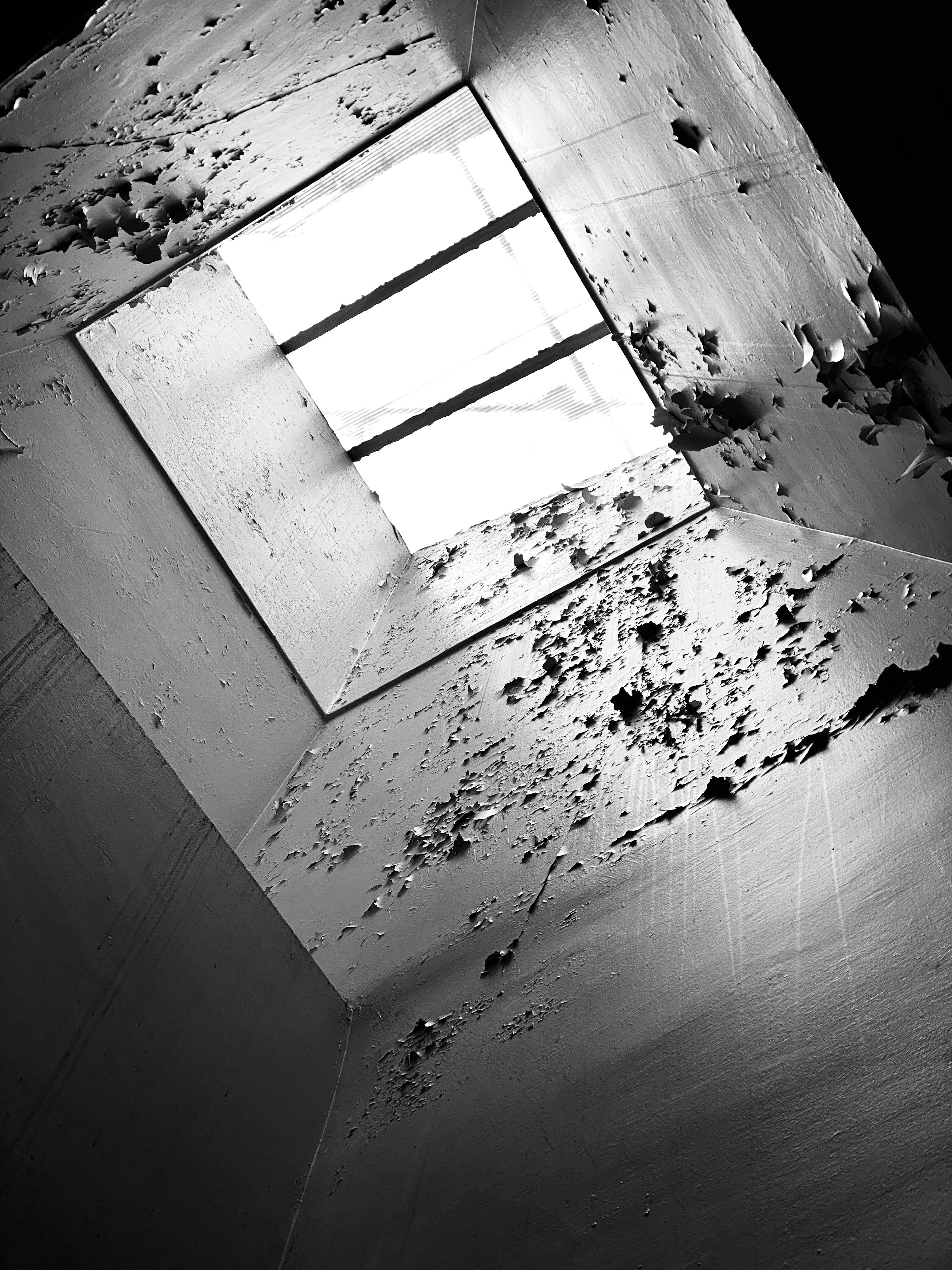 Light filtering through a dusty skylight, revealing peeling walls in a neglected space.
