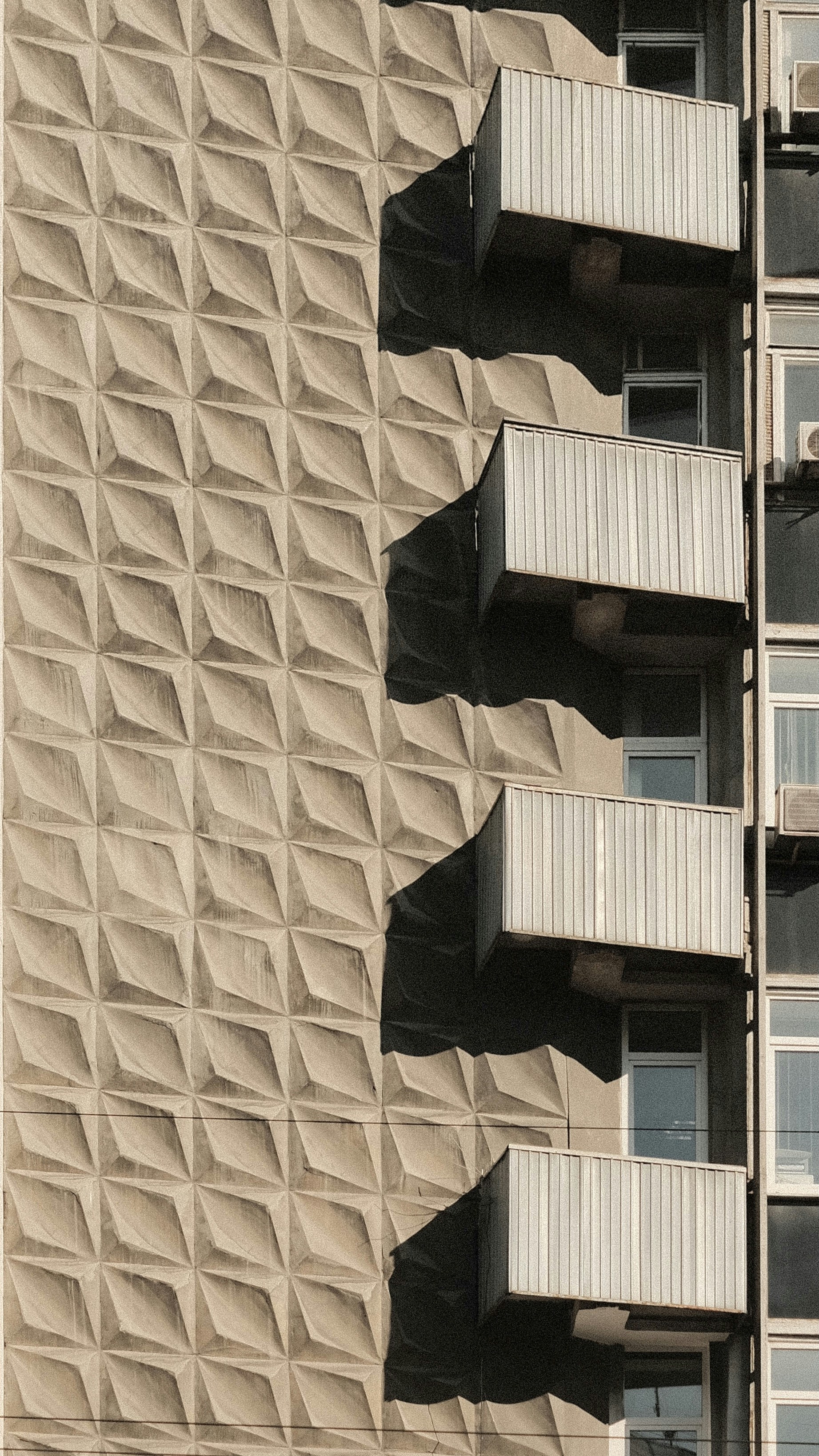 Textured building facade with protruding balconies casting distinctive shadows, highlighting architectural design.