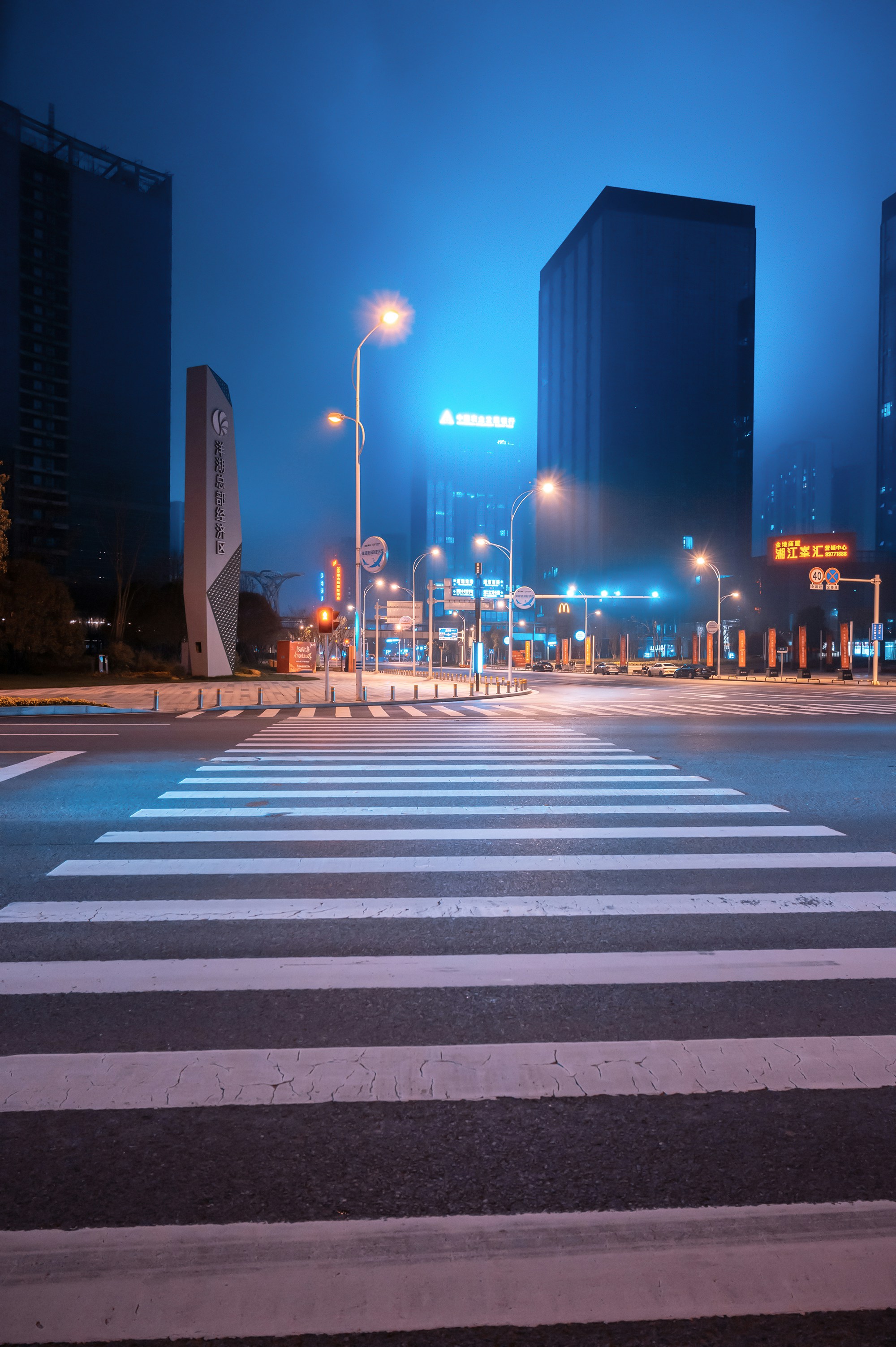 Illuminated crosswalk leading into a foggy urban landscape with towering skyscrapers in the background.