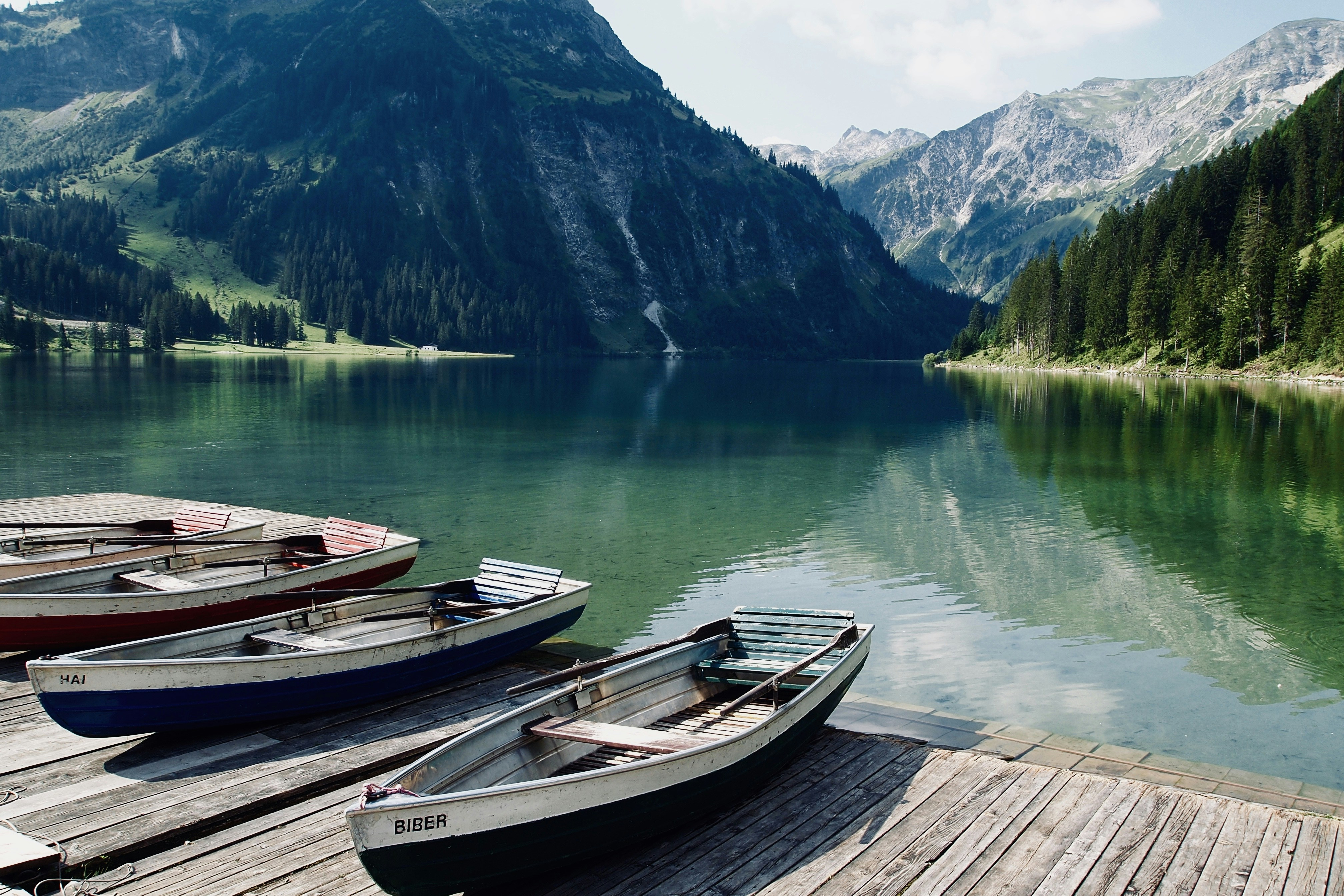 Rowboats lined up on a wooden dock beside a tranquil lake, surrounded by majestic mountains and lush greenery.