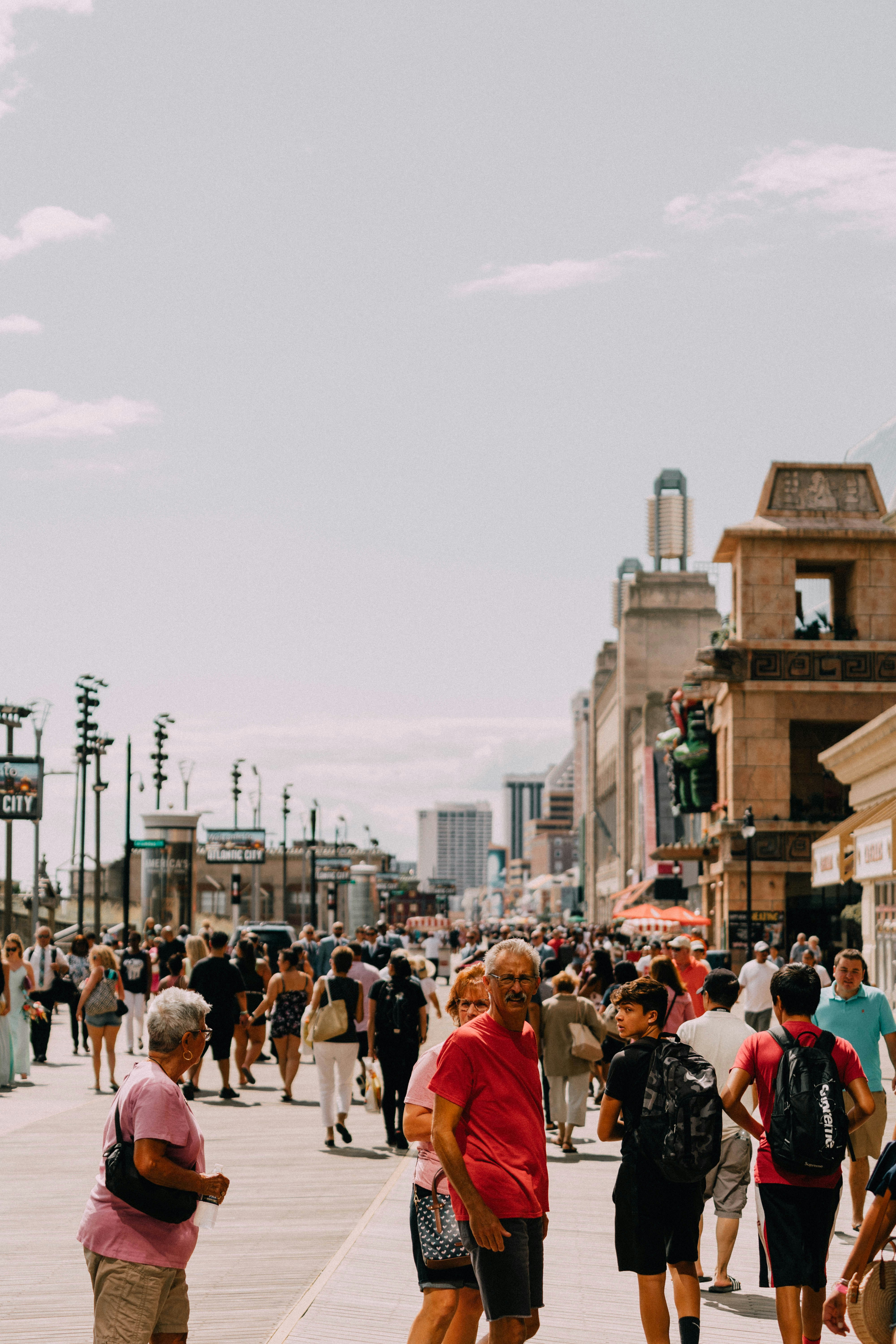 Crowd of people enjoying a vibrant boardwalk scene filled with shops and attractions. A mix of leisure and activity defines the atmosphere.