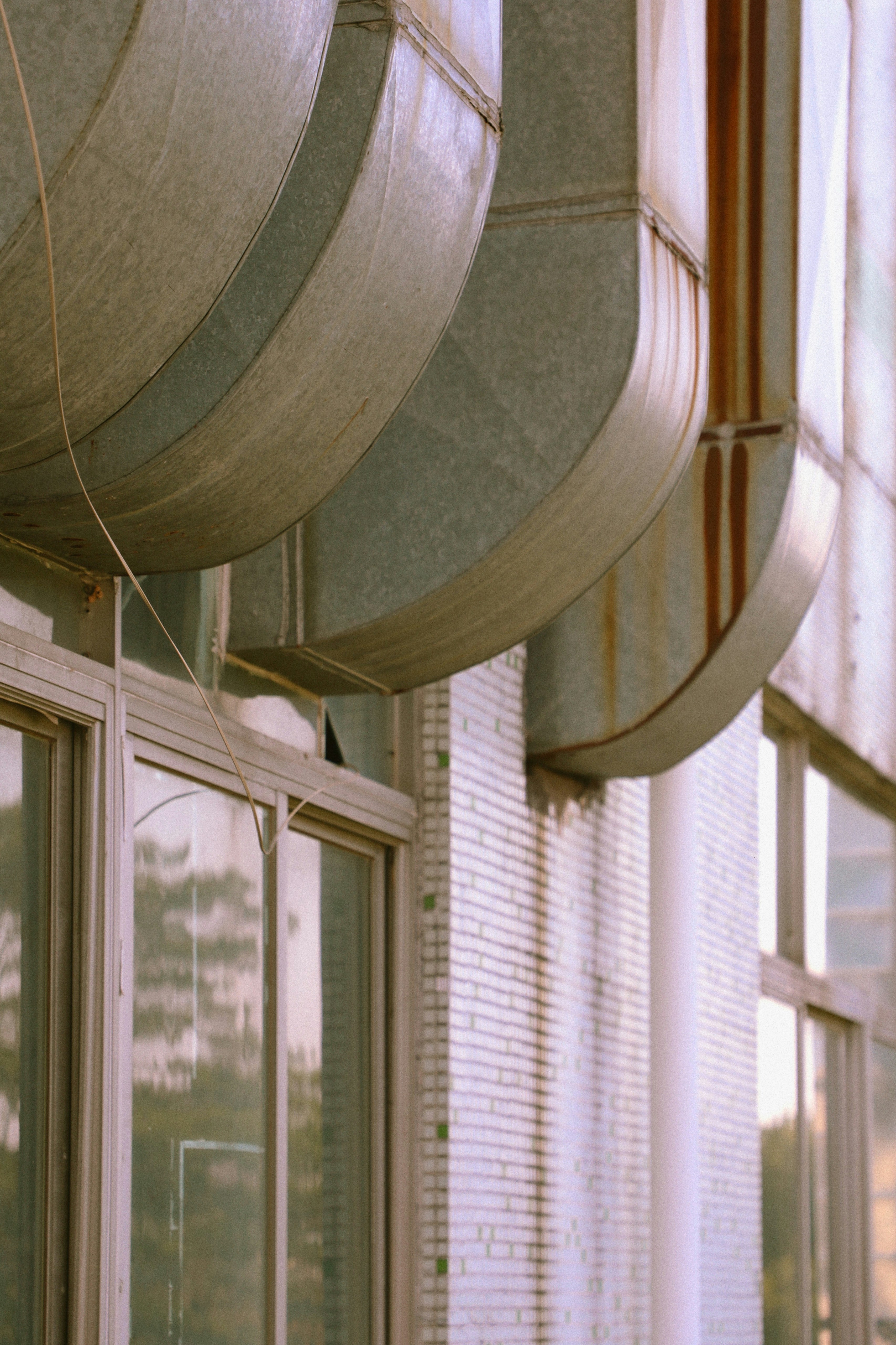 Weathered metal ducts protruding from a building's facade, juxtaposed against a backdrop of reflective glass and aged bricks.