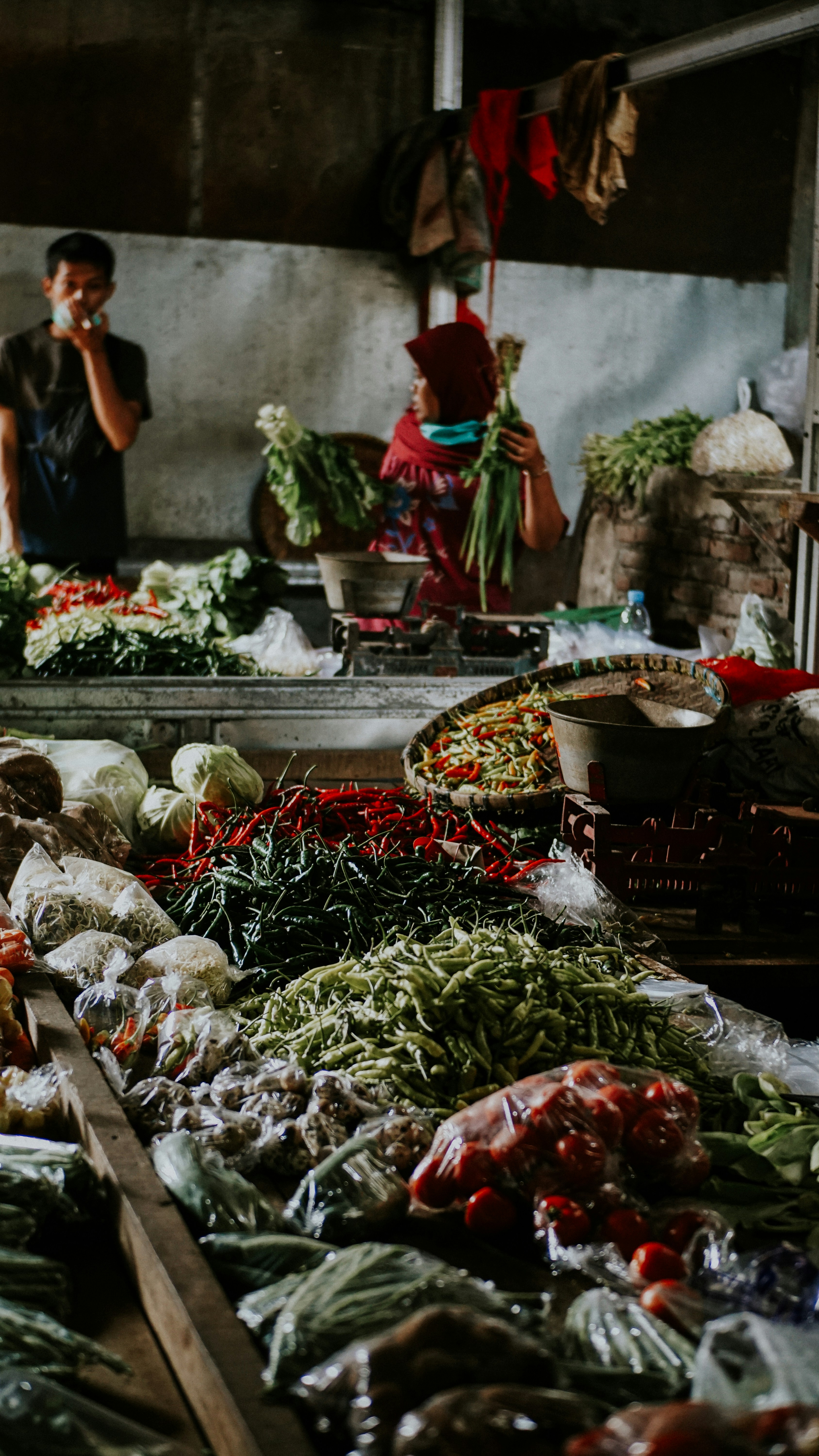 Vibrant array of fresh vegetables and herbs displayed at a bustling market, with vendors engaged in lively trade.