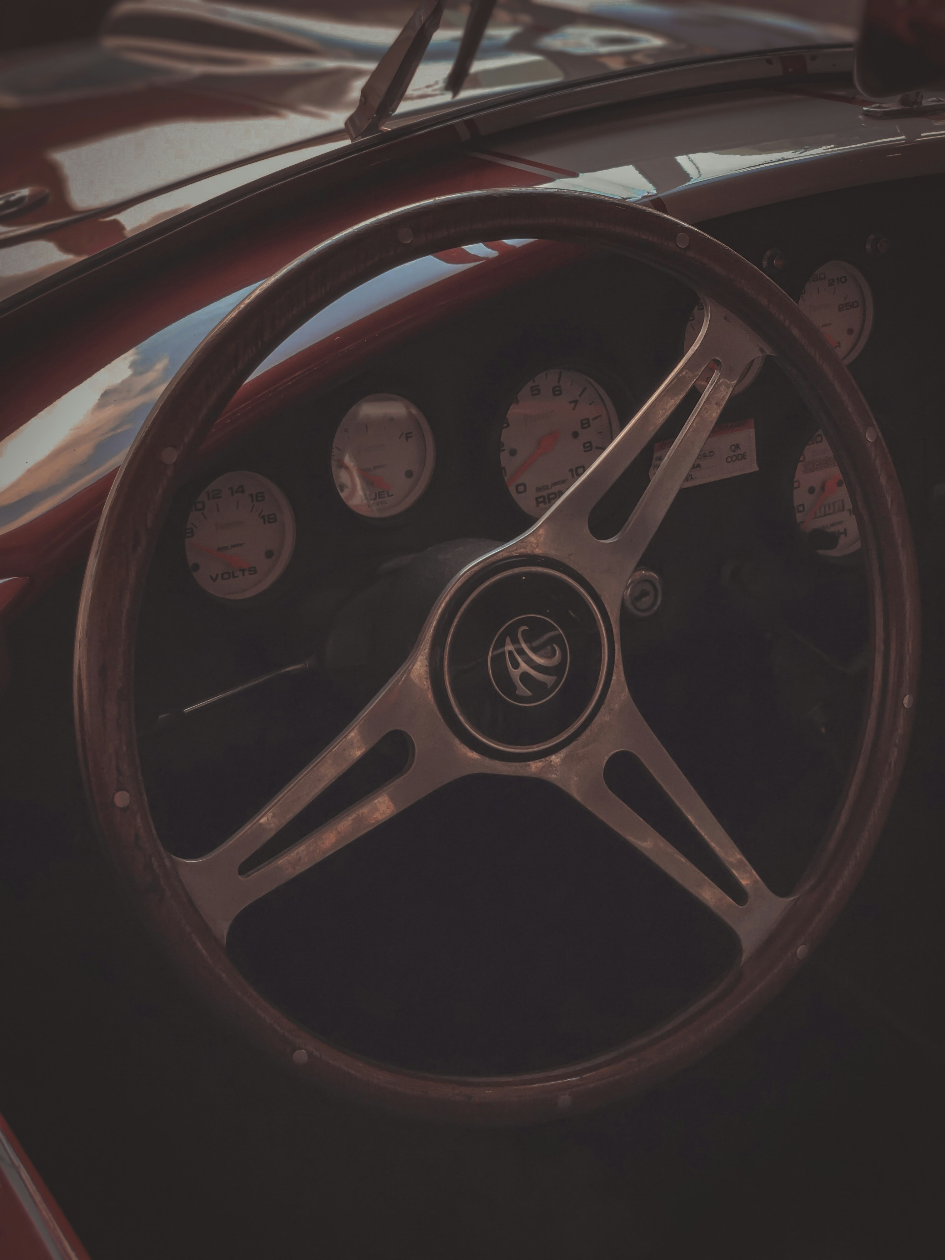 Close-up of a vintage car's steering wheel and dashboard, showcasing classic gauges and a polished wooden finish.