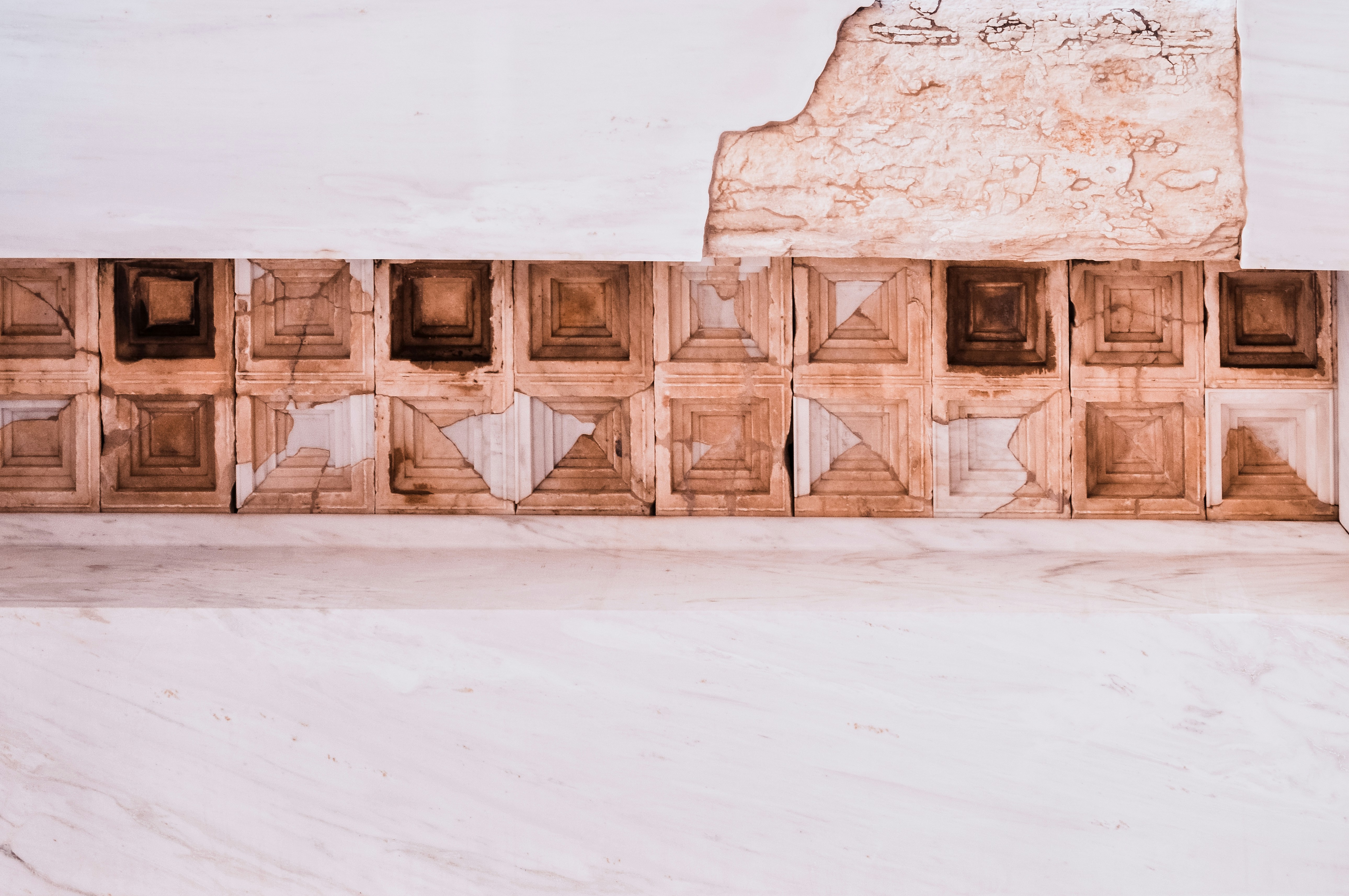 Rhythmic Wooden Squares: A Row of Carved Panels Against a Cracked White Wall