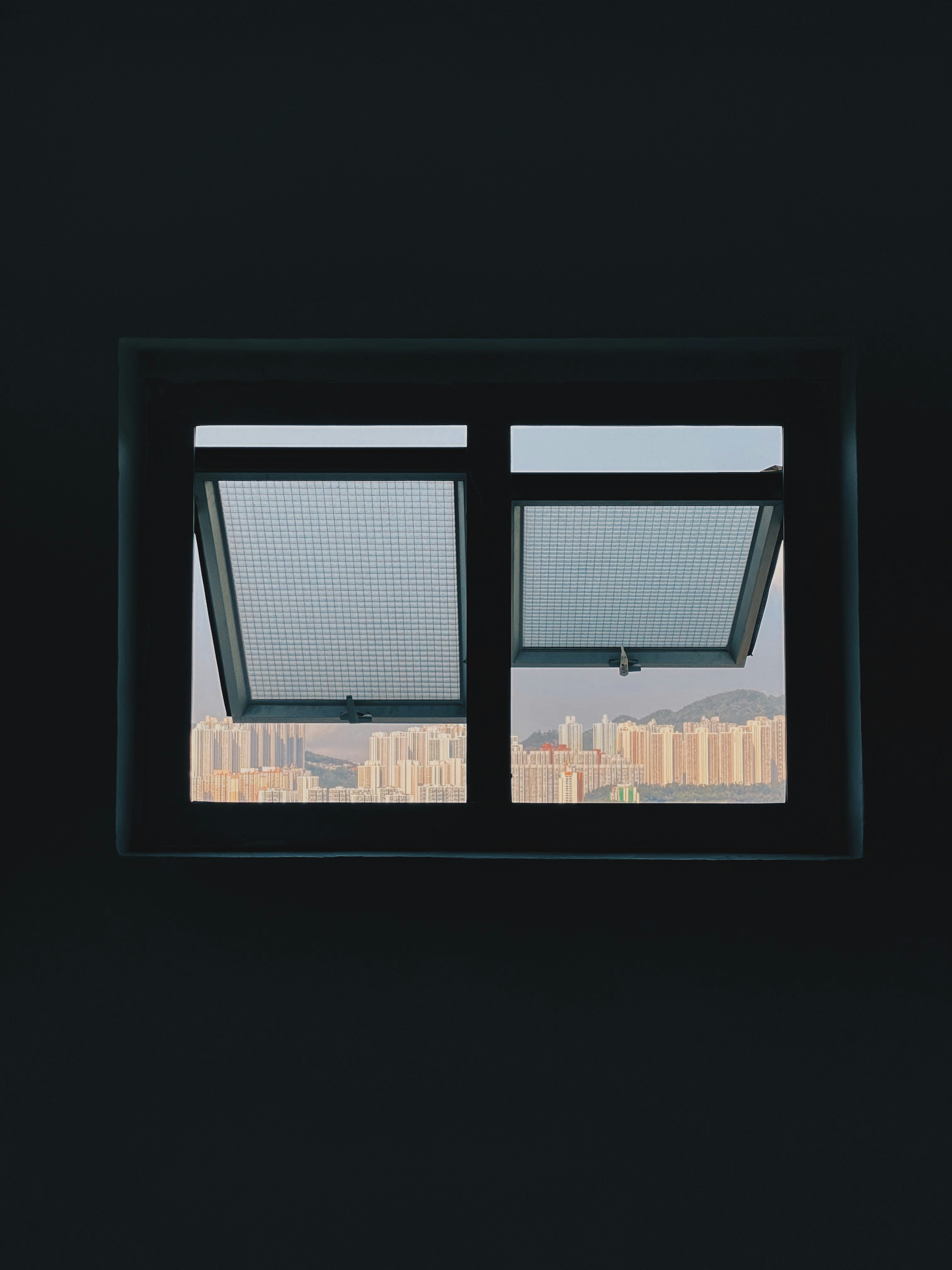 Open window revealing a city skyline with modern buildings against a soft backdrop of mountains.